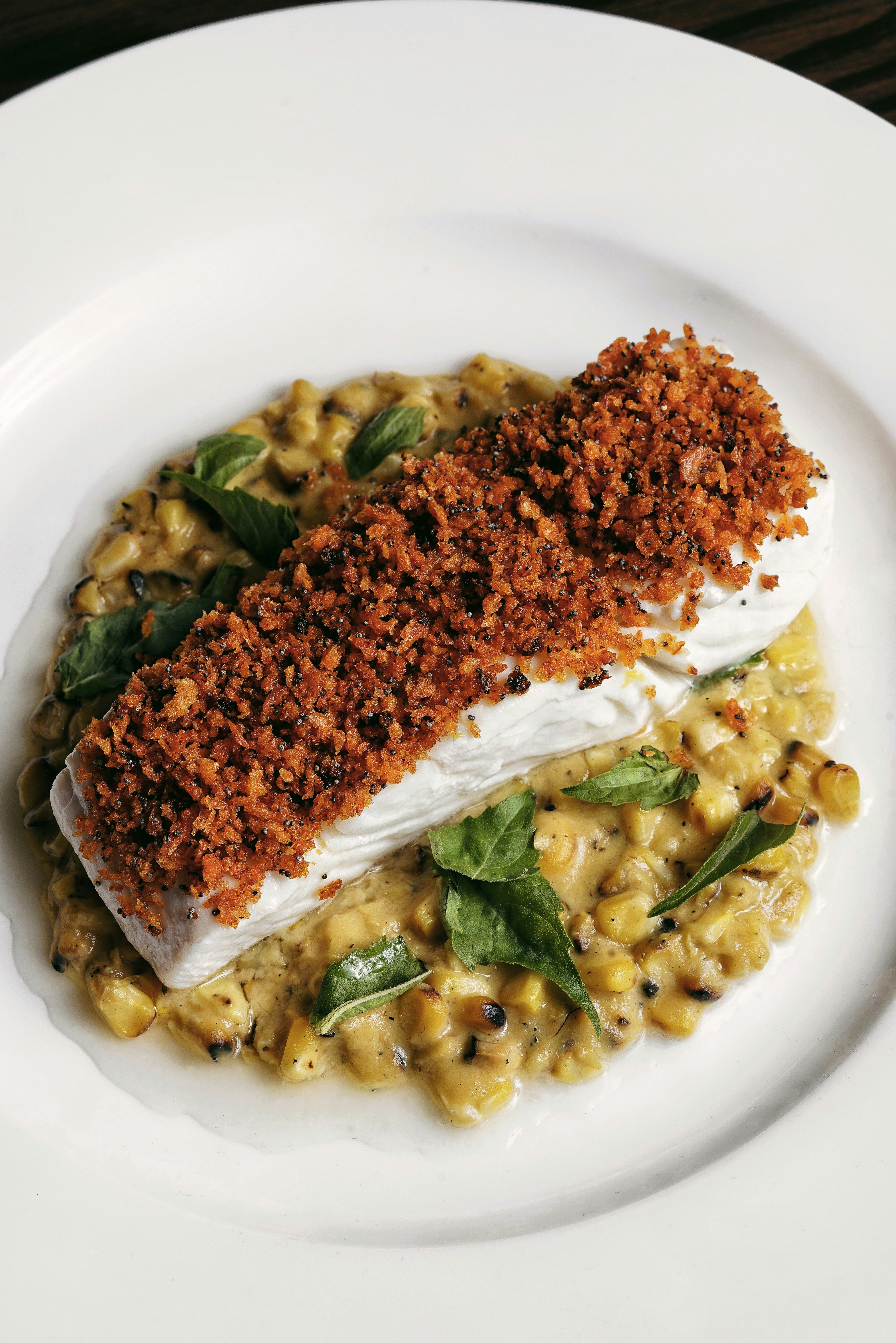 Fish fillet topped with a golden breadcrumb crust on a bed of creamy corn and fresh herbs.
