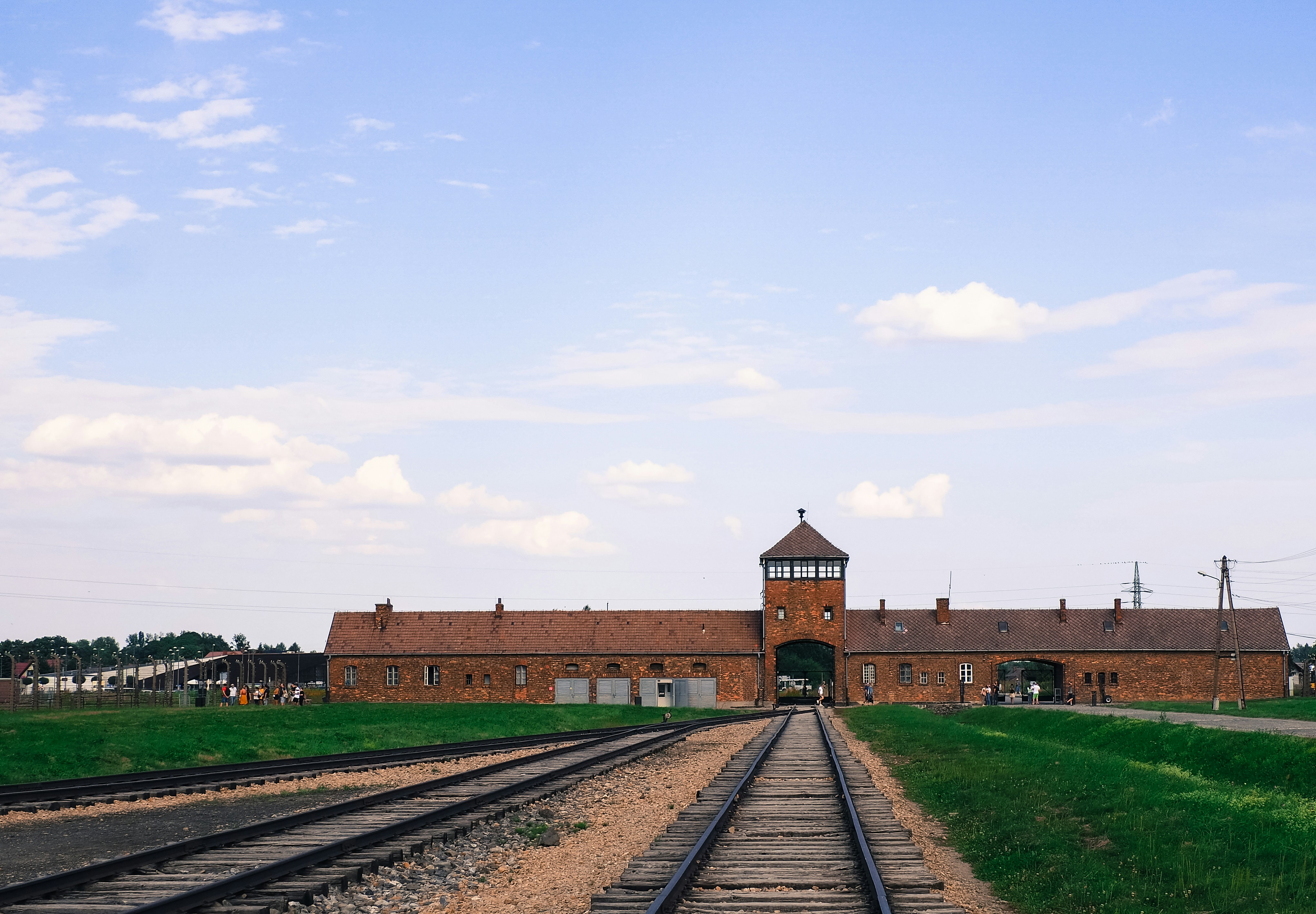 Railway tracks leading to the entrance of Auschwitz-Birkenau under a blue sky.