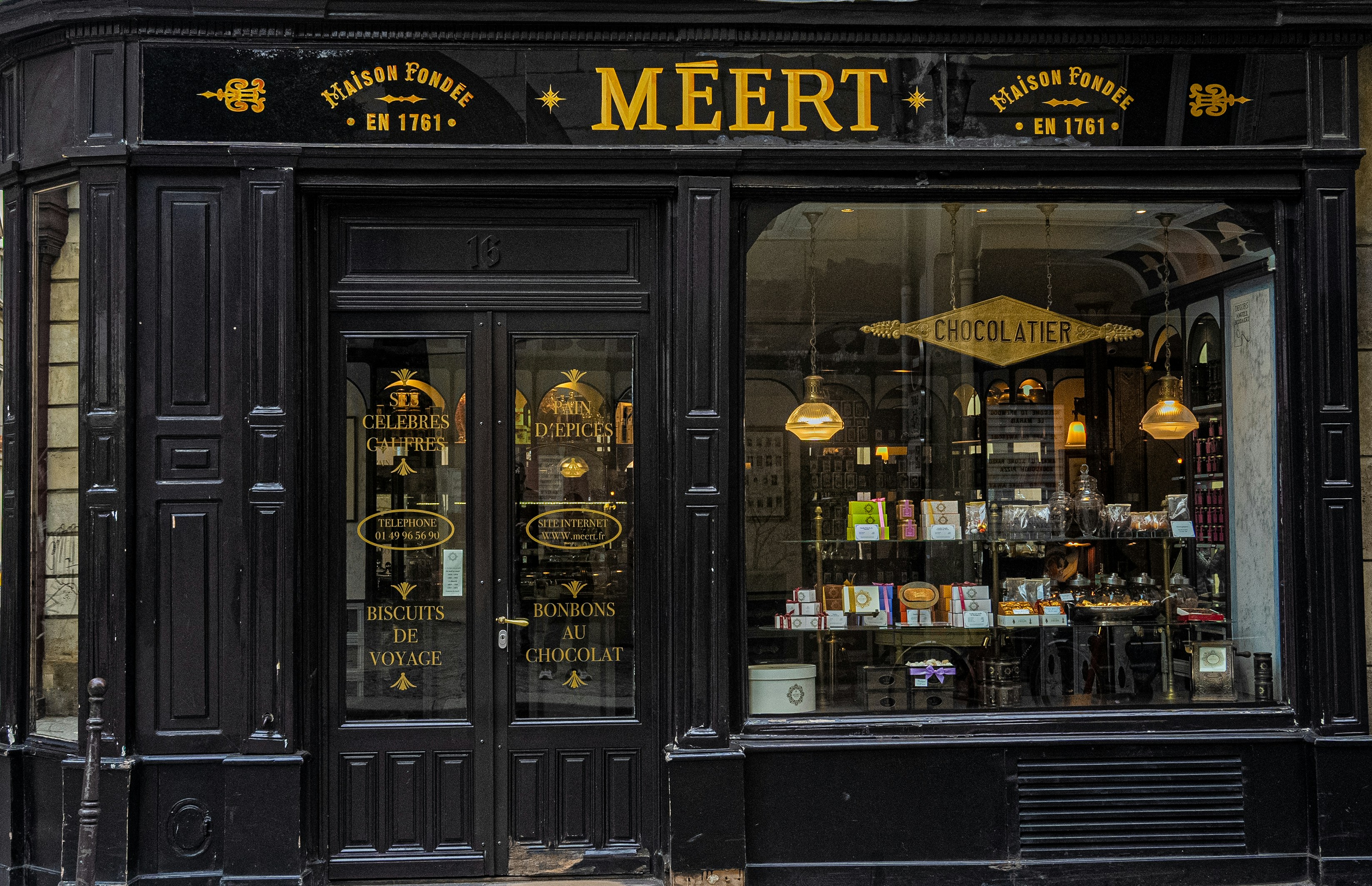 Elegant storefront of Meert, a historic chocolatier established in 1761, showcasing ornate signage and inviting window displays filled with confections.