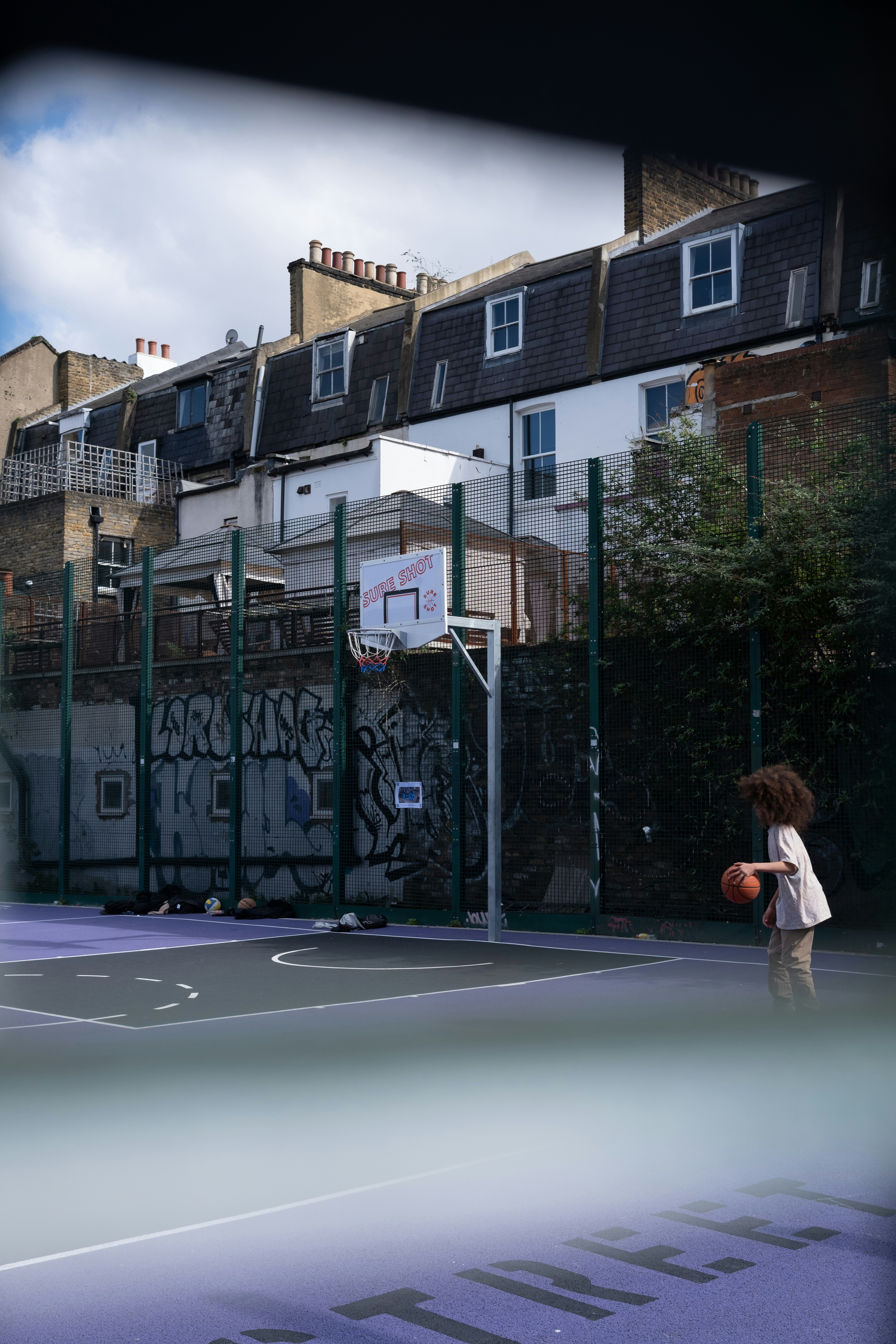 Young child preparing to shoot a basketball on a vibrant court surrounded by urban graffiti and buildings.