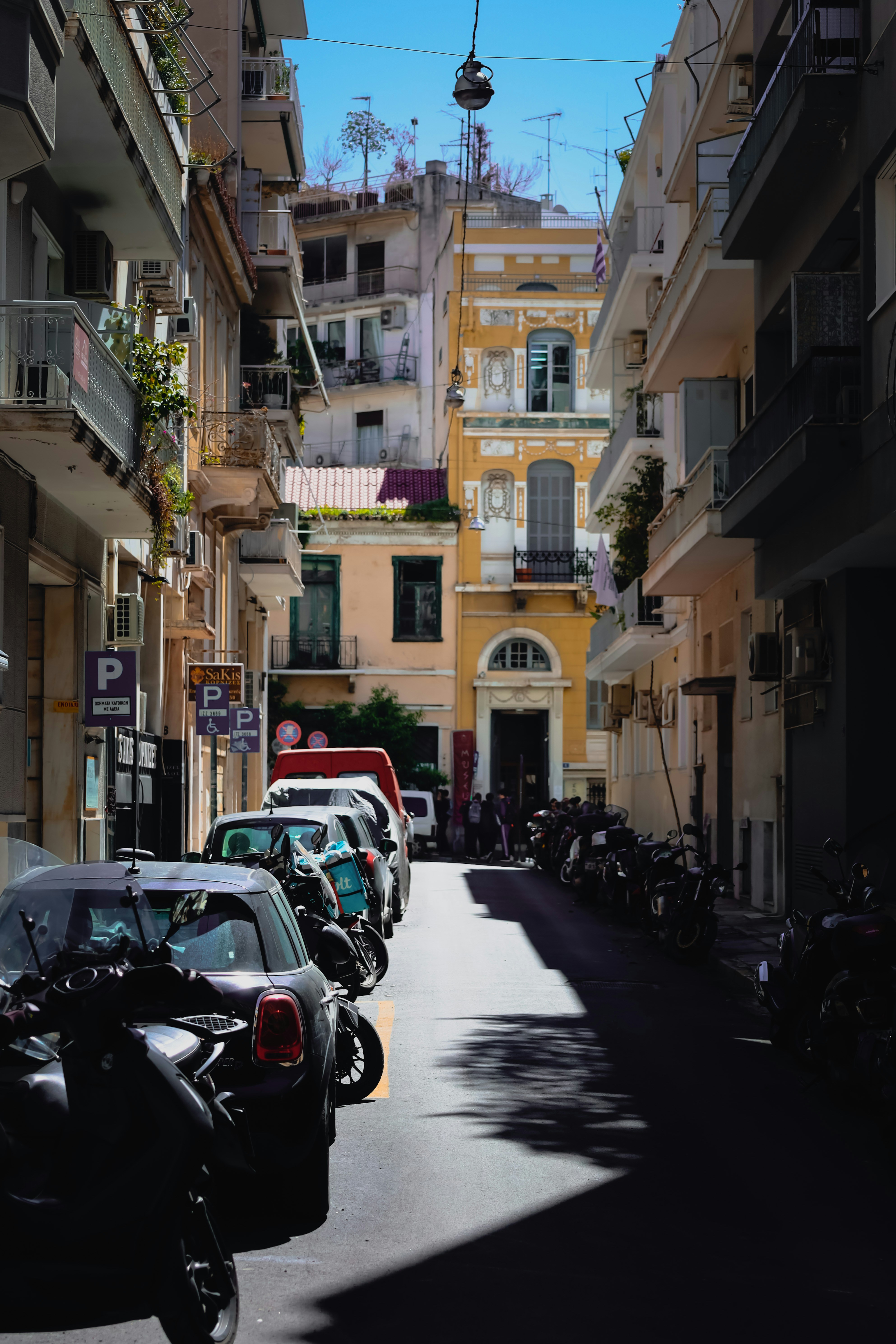 The Yellow Gatekeeper: Sunlit Facade Framing a Scooter-Lined Urban Street
