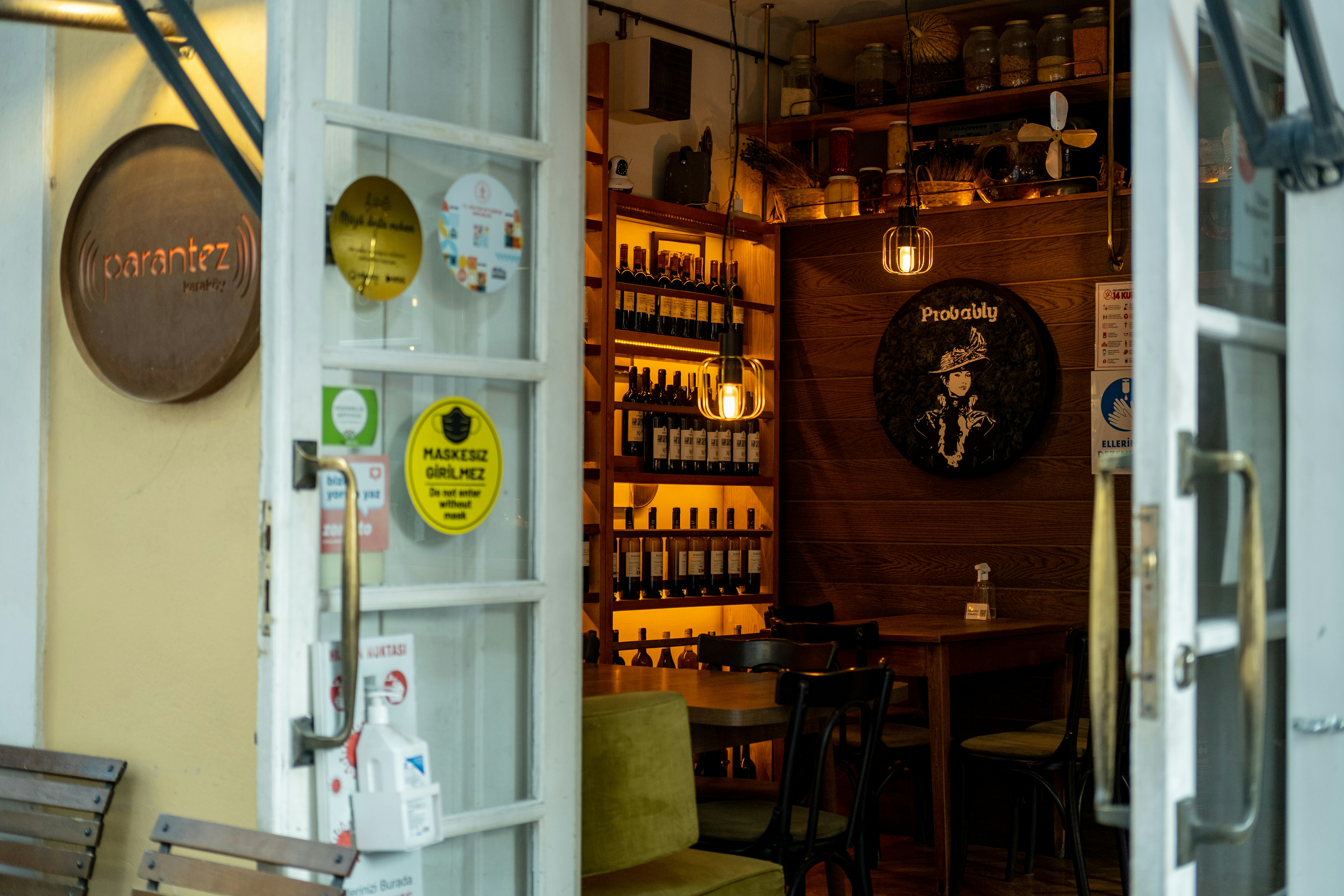 Open café entrance with warm interior lighting and wine display on shelves.