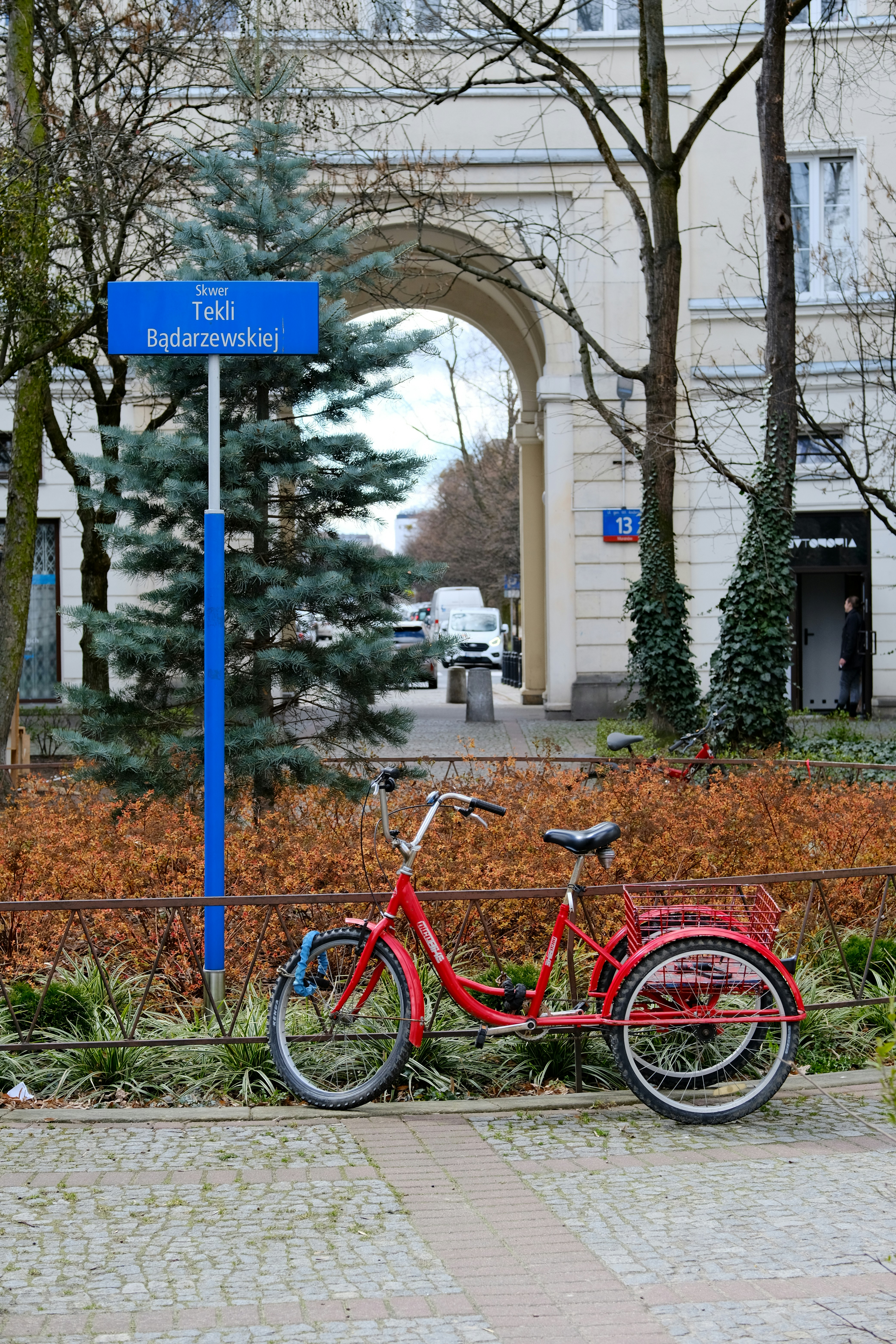 Red cargo bicycle by a blue street sign beneath a stone archway
