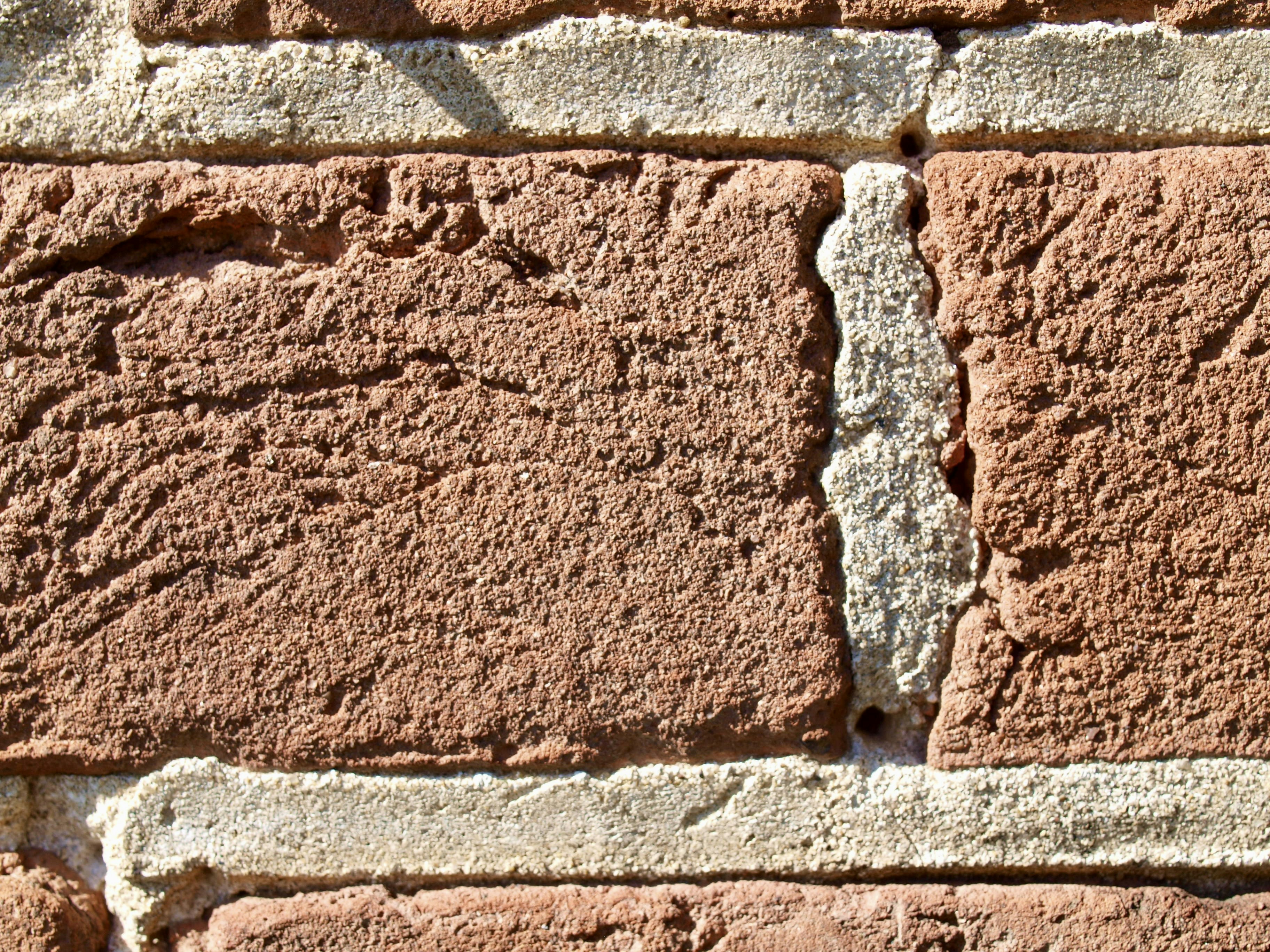 A horizontal close up of an exterior wall of hand-fired red clay bricks with mortar in between.