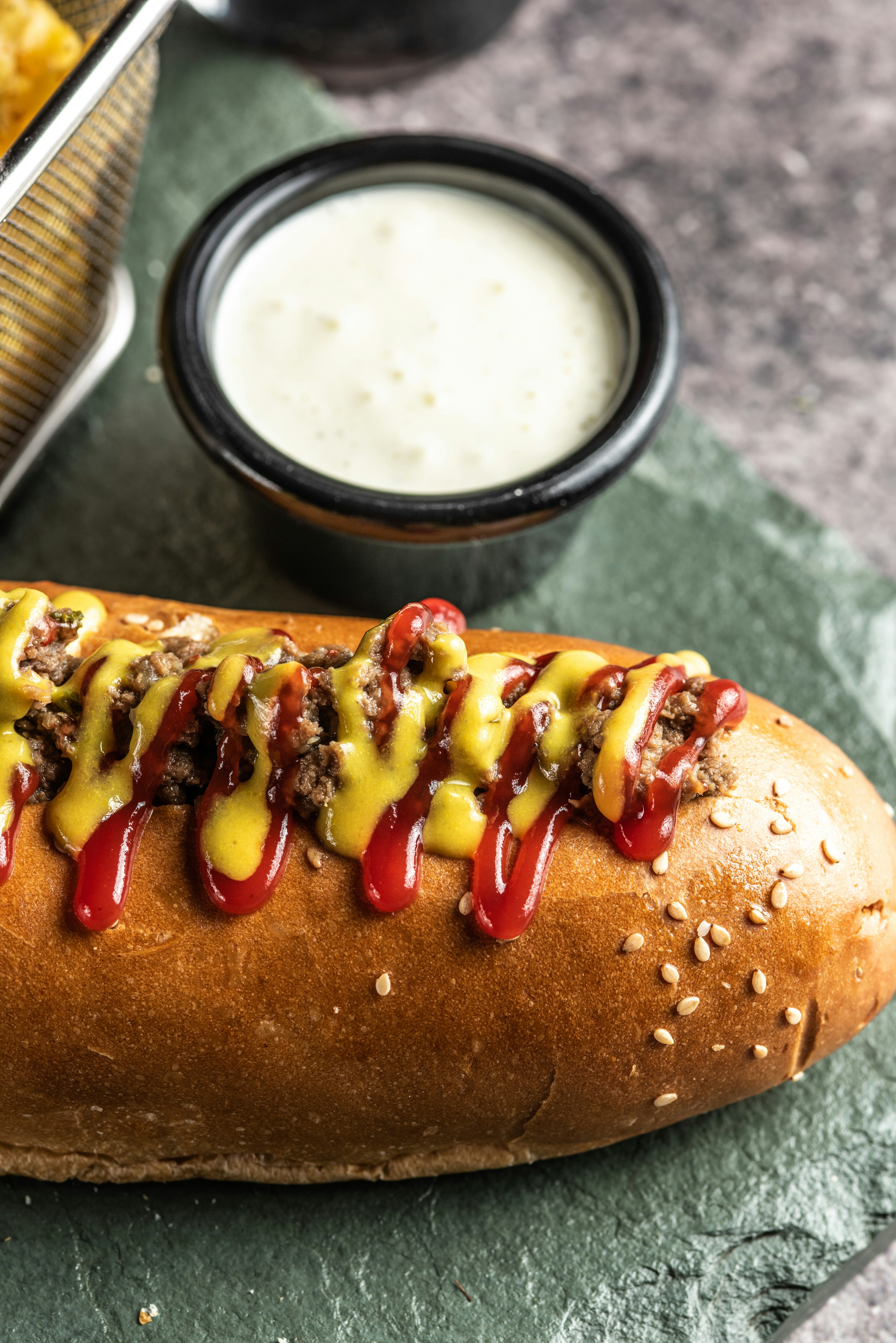 Sauce-Stripe Dream: Close-Up on a Loaded Sesame Bun Hot Dog