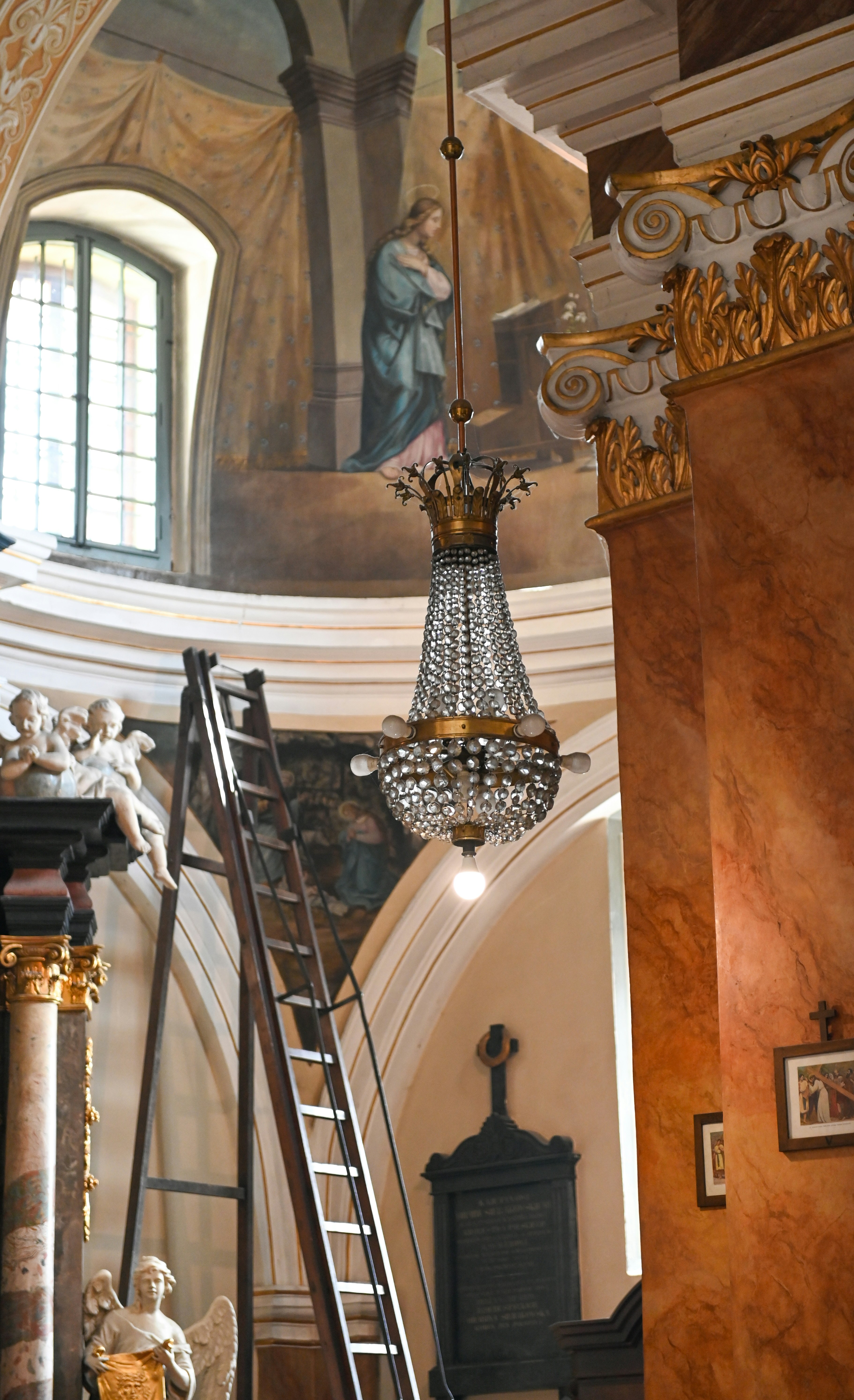 Crystal Chandelier Amid Baroque Light: A Ladder, Statues, and Golden Detailing
