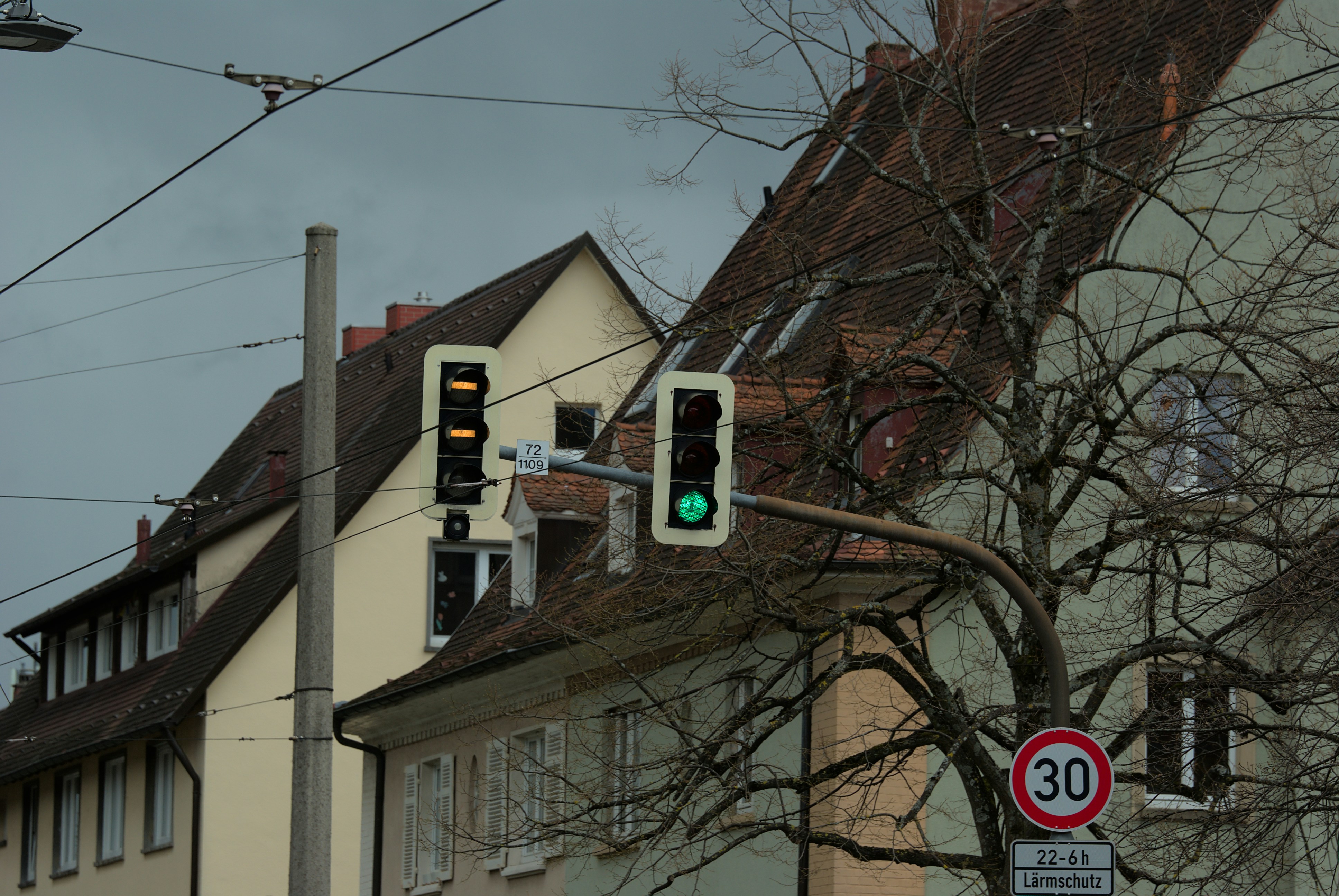 Traffic lights signaling green amidst a backdrop of residential buildings and a cloudy sky.