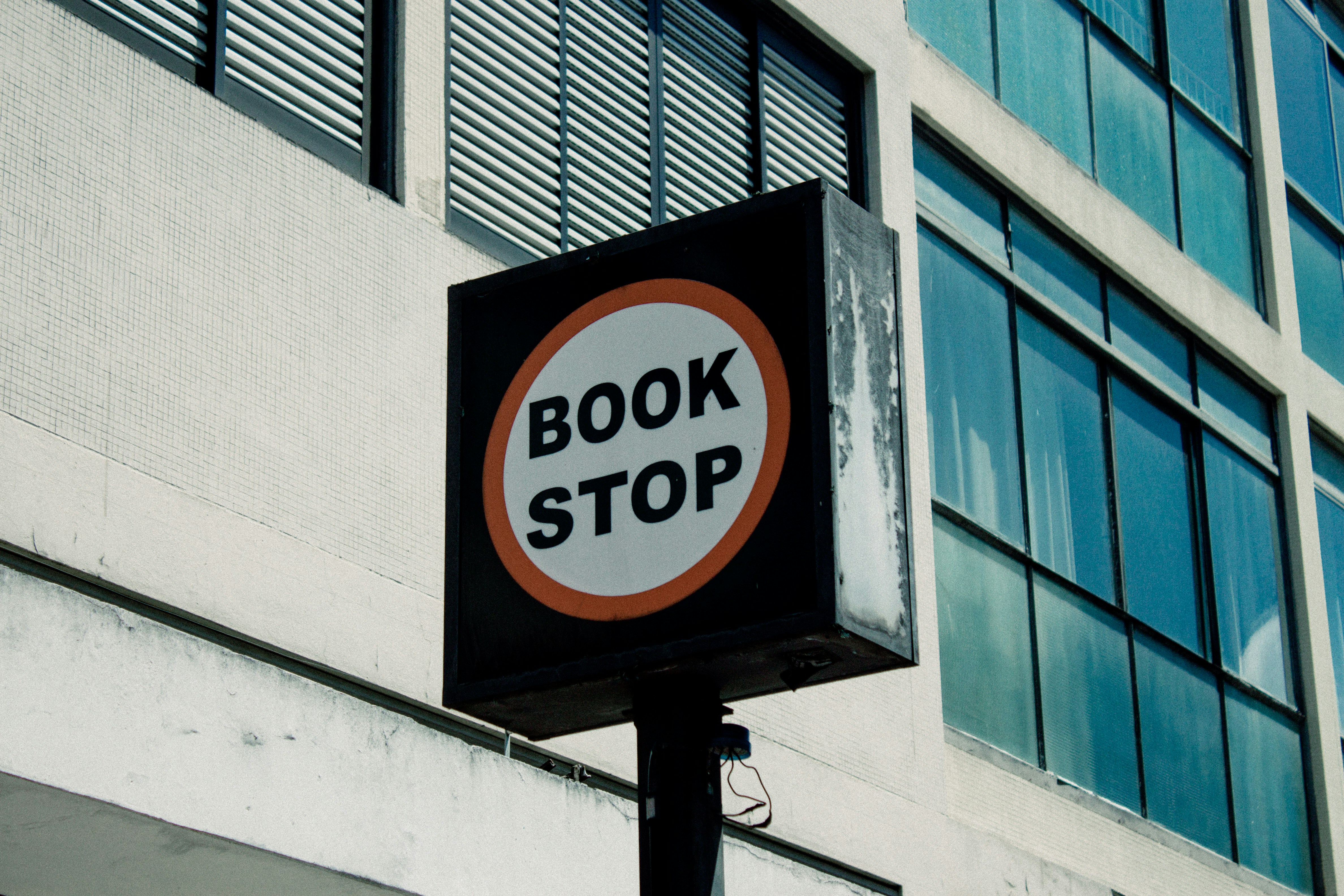 Sign reading 'Book Stop' against a modern building facade with glass windows.