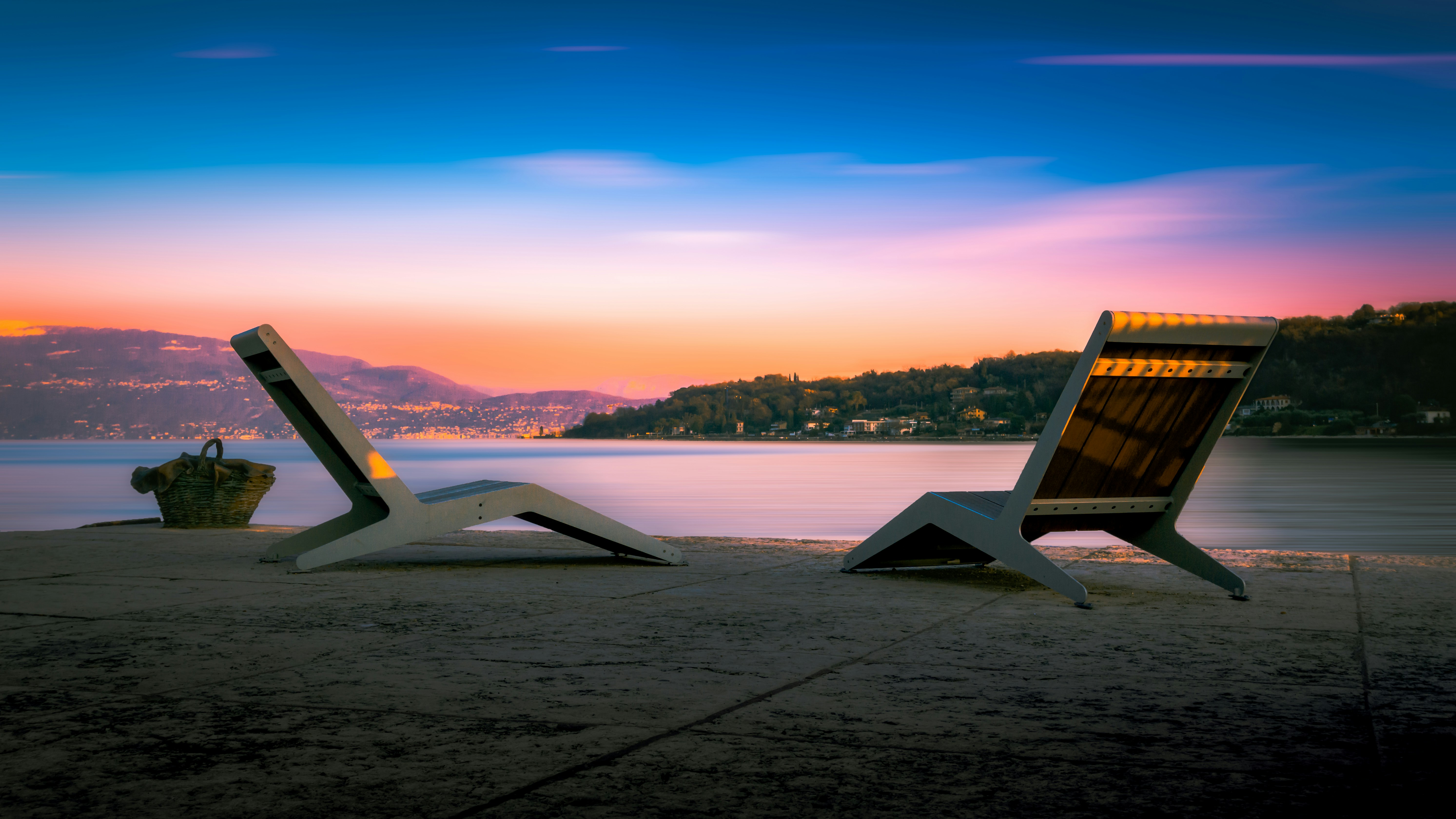 Two lounge chairs facing a tranquil sea under a vibrant sunset sky.