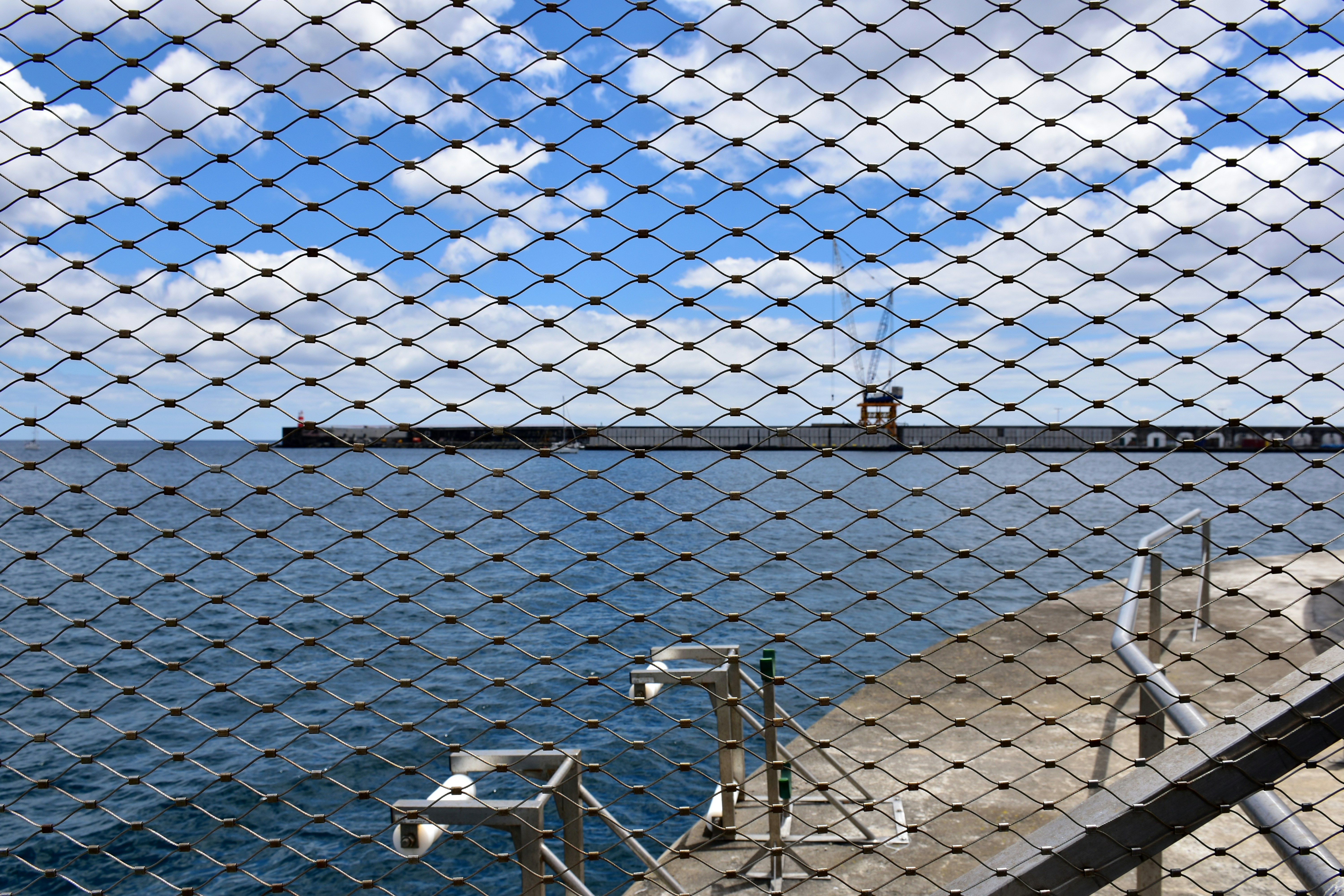 Harbor Crane Framed by Diamond Mesh Against a Calm Sea Horizon