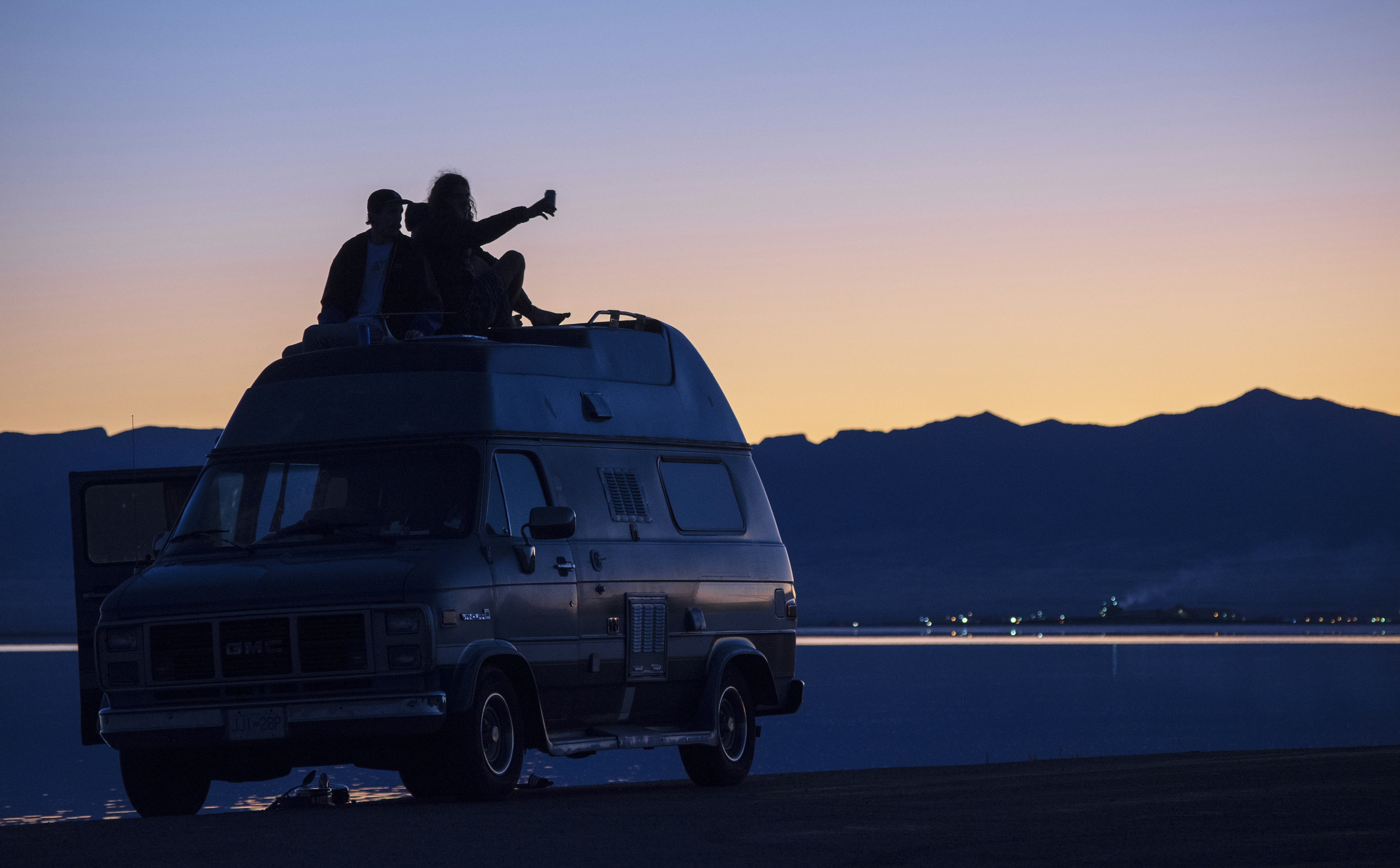 People saying cheers on the roof of a van enjoying the sunset over the Bonneville Salt Flats in Utah.