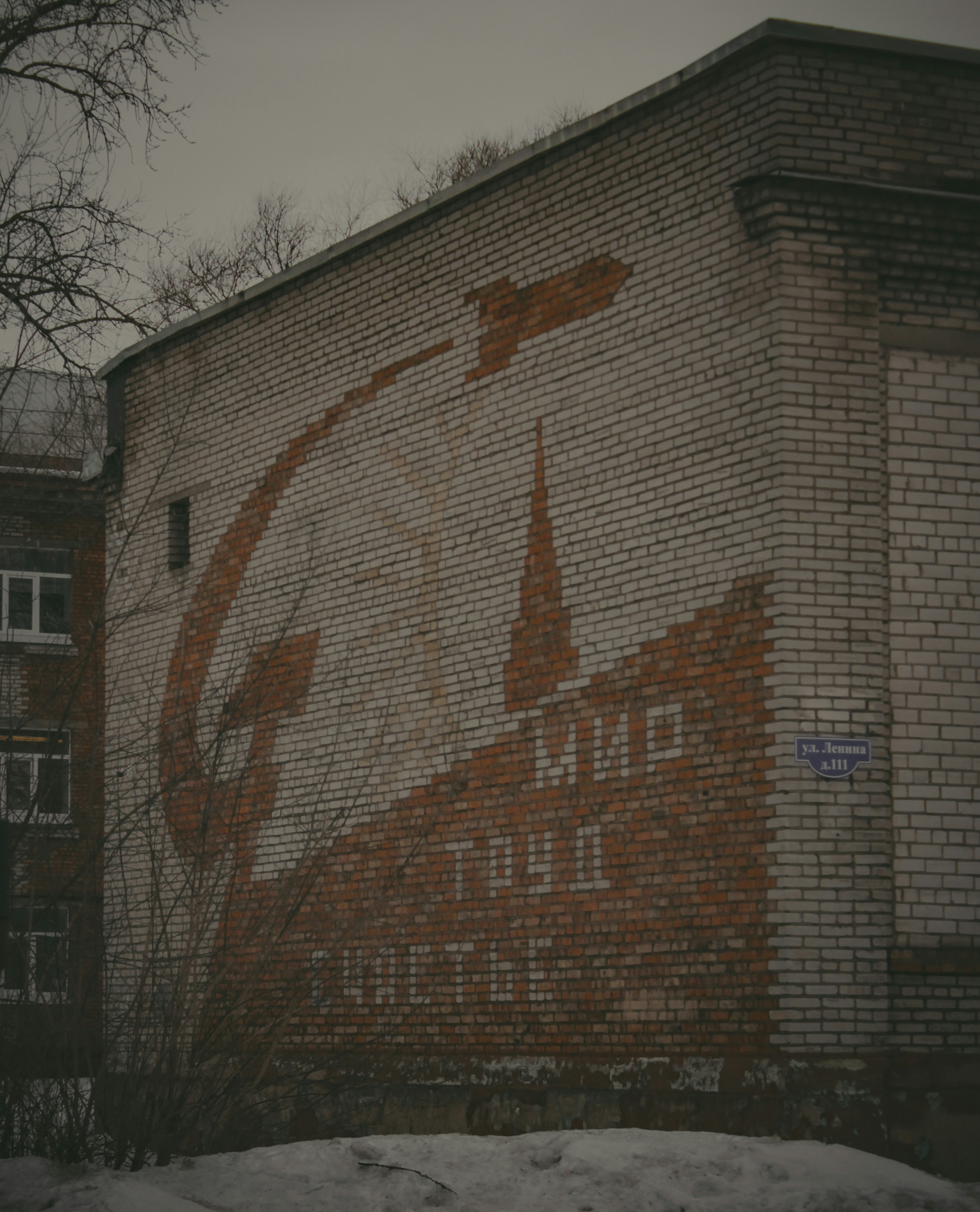 Faded red mural on a snow-dusted brick wall