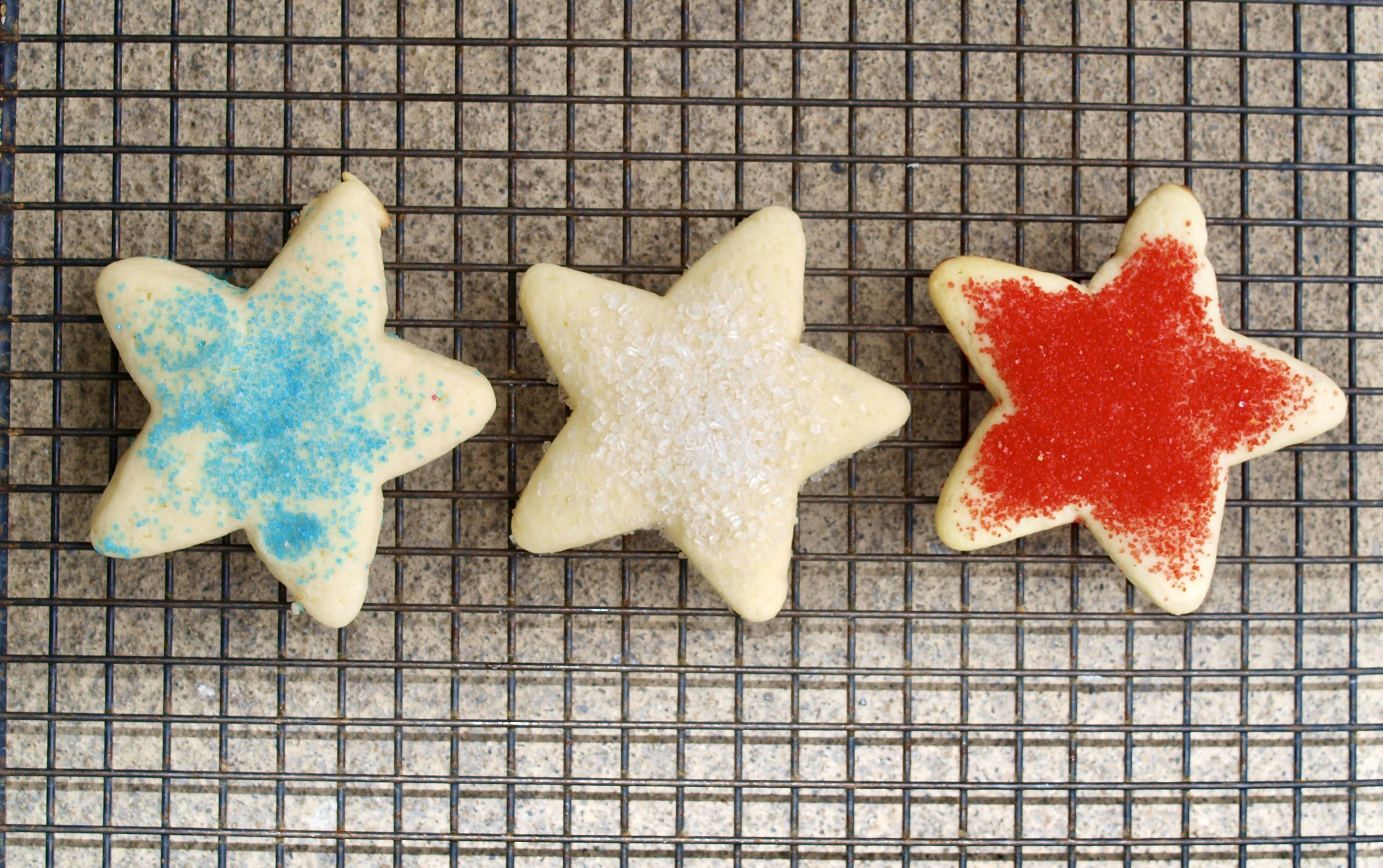 A photograph of three sugar stars with blue, white, and red icing resting on a checkered grid background, highlighting color contrast and texture.