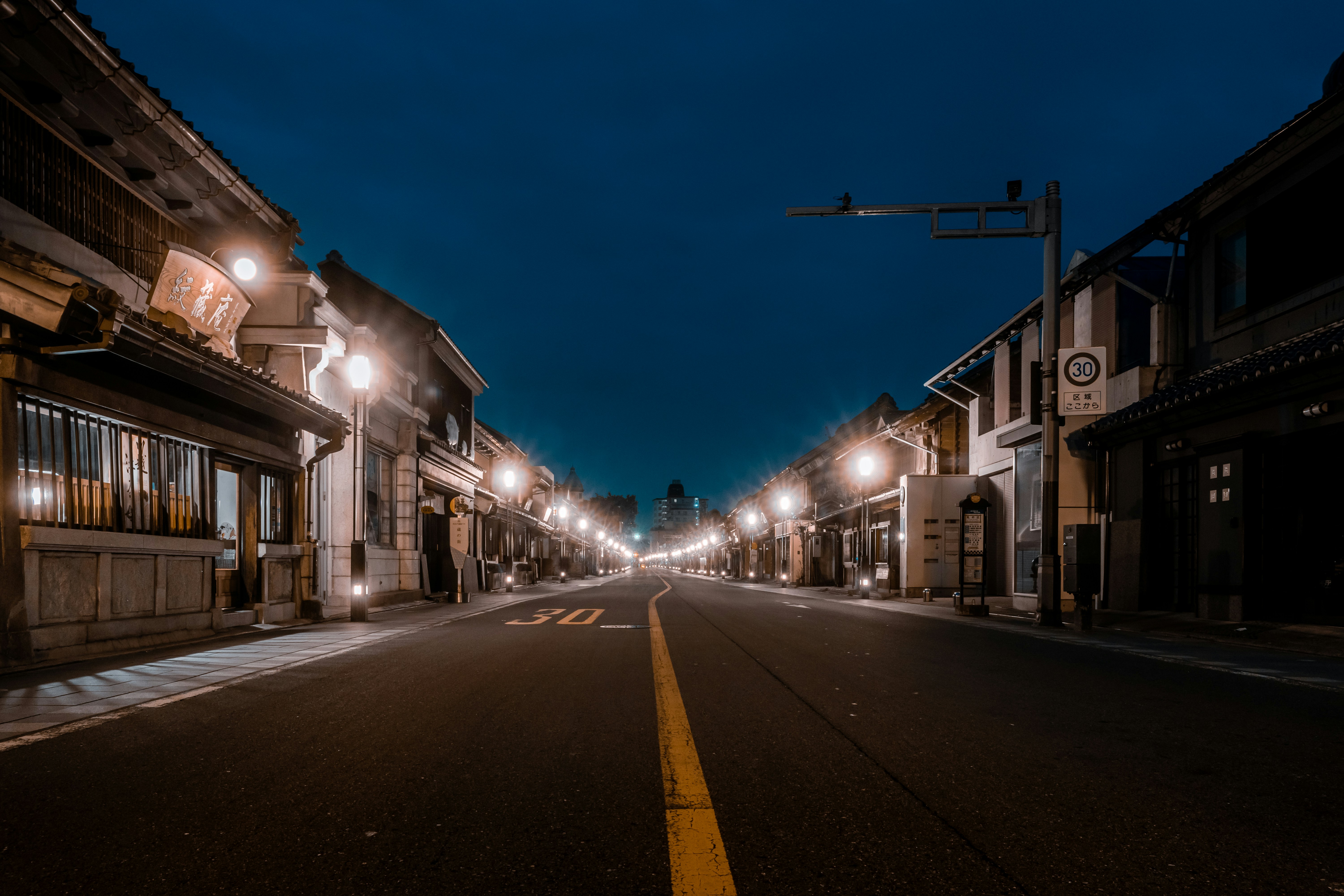 Empty nighttime street with traditional Japanese buildings and glowing streetlights.