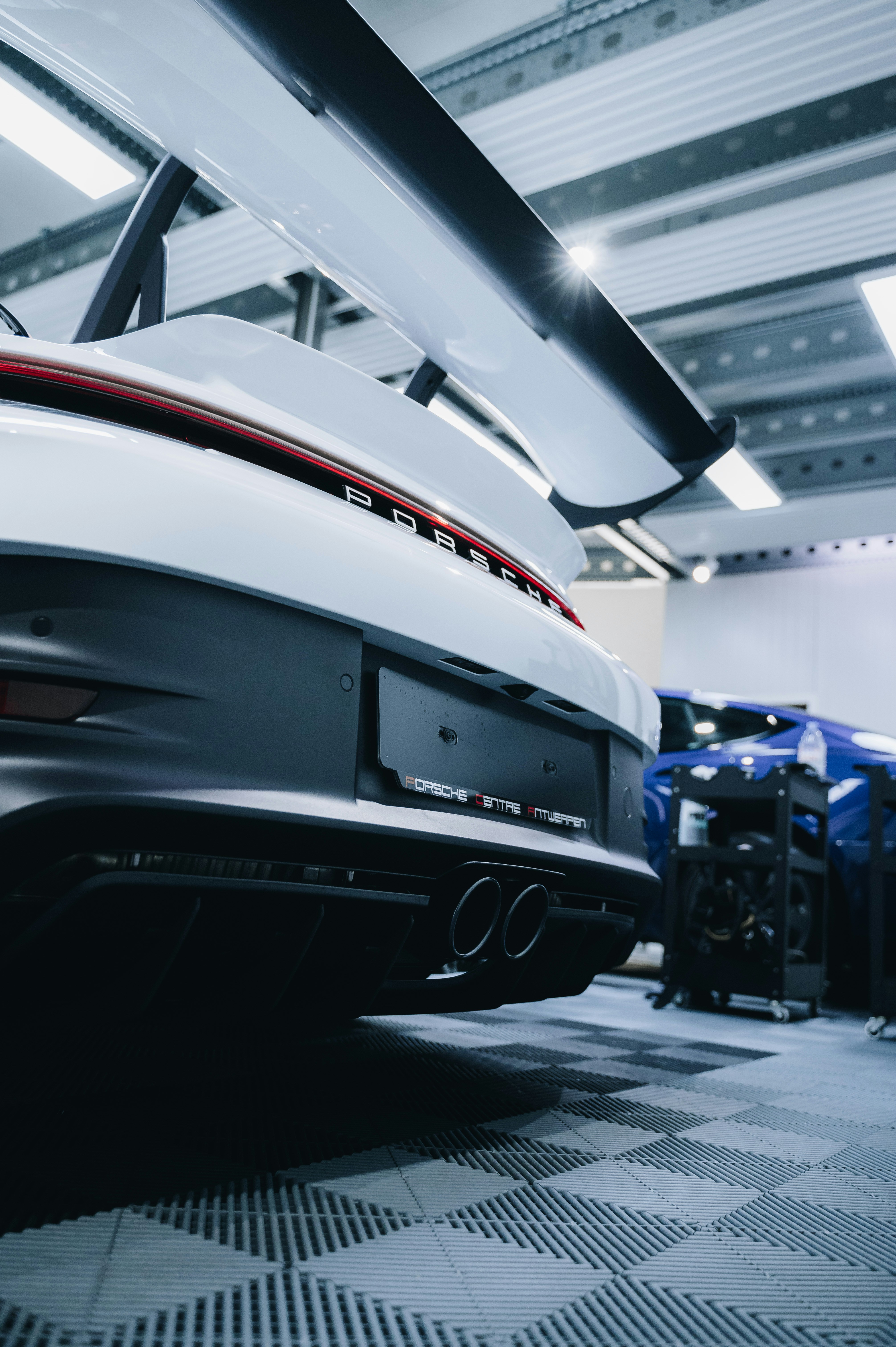 Rear view of a Porsche sports car showcasing its aerodynamic design and dual exhausts in a modern garage setting.