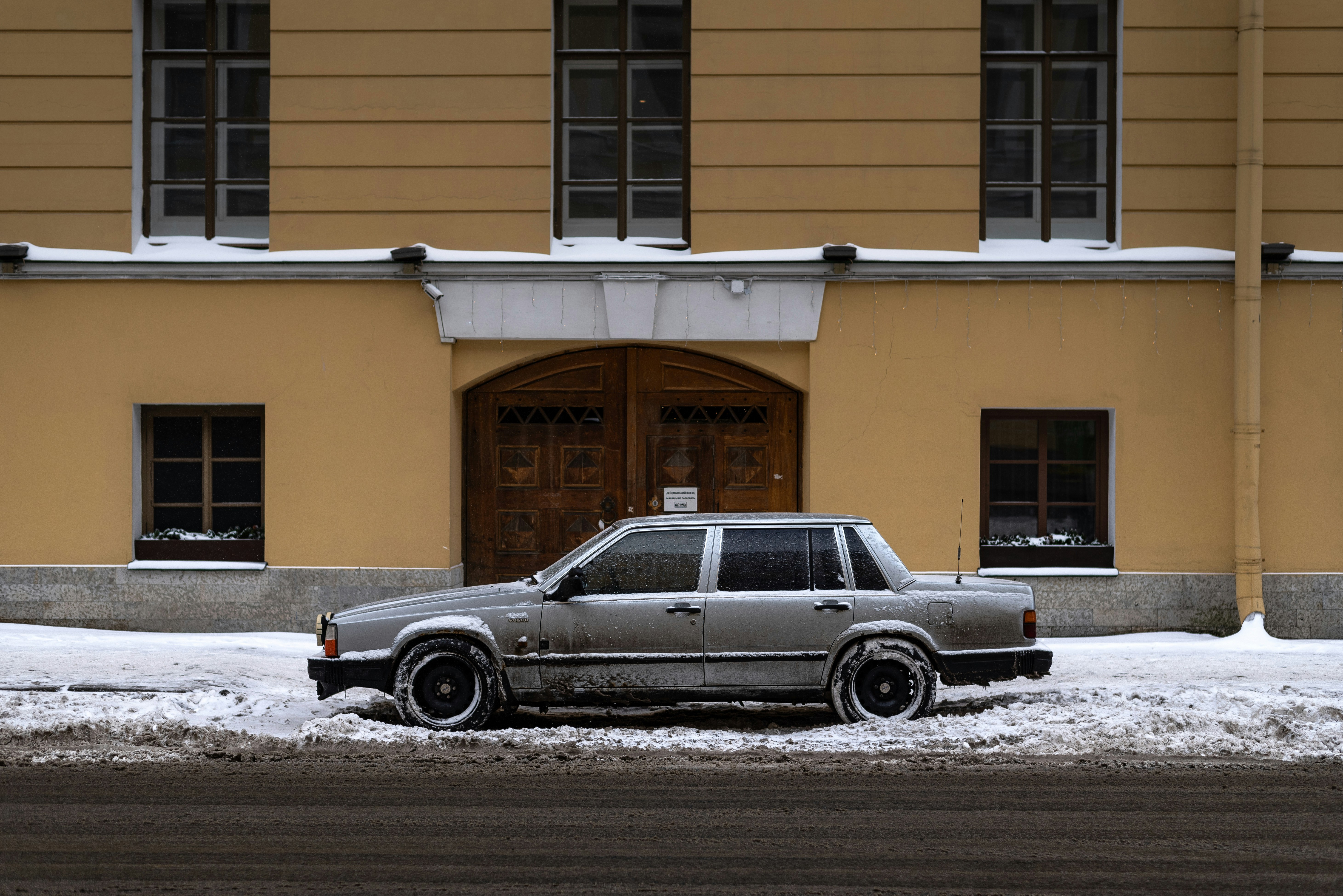 Snow-Covered Sedan Framed by a Warm Yellow Facade