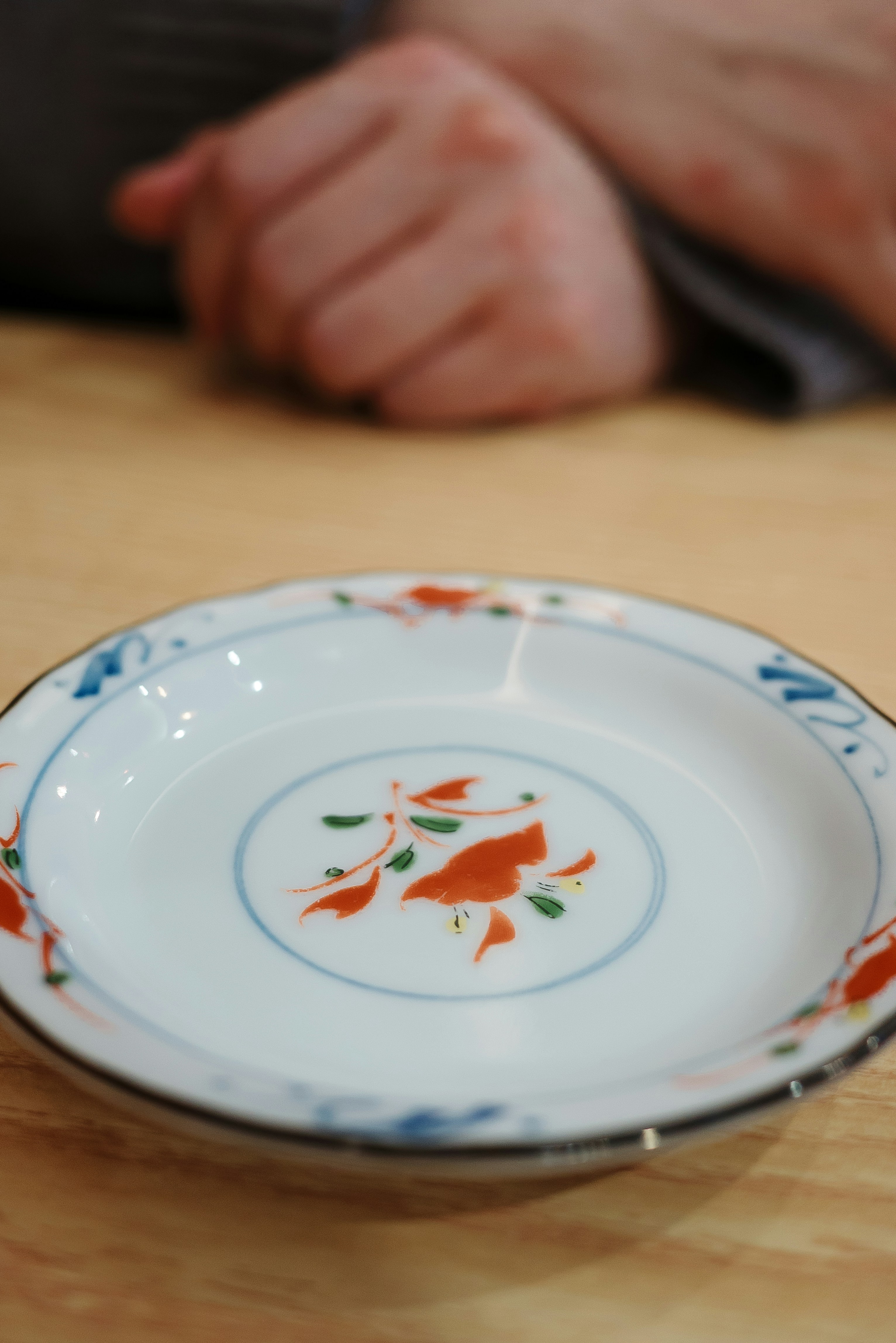 Koi on Ceramic Plate: A Focused Center Amidst Soft-Blurred Hands