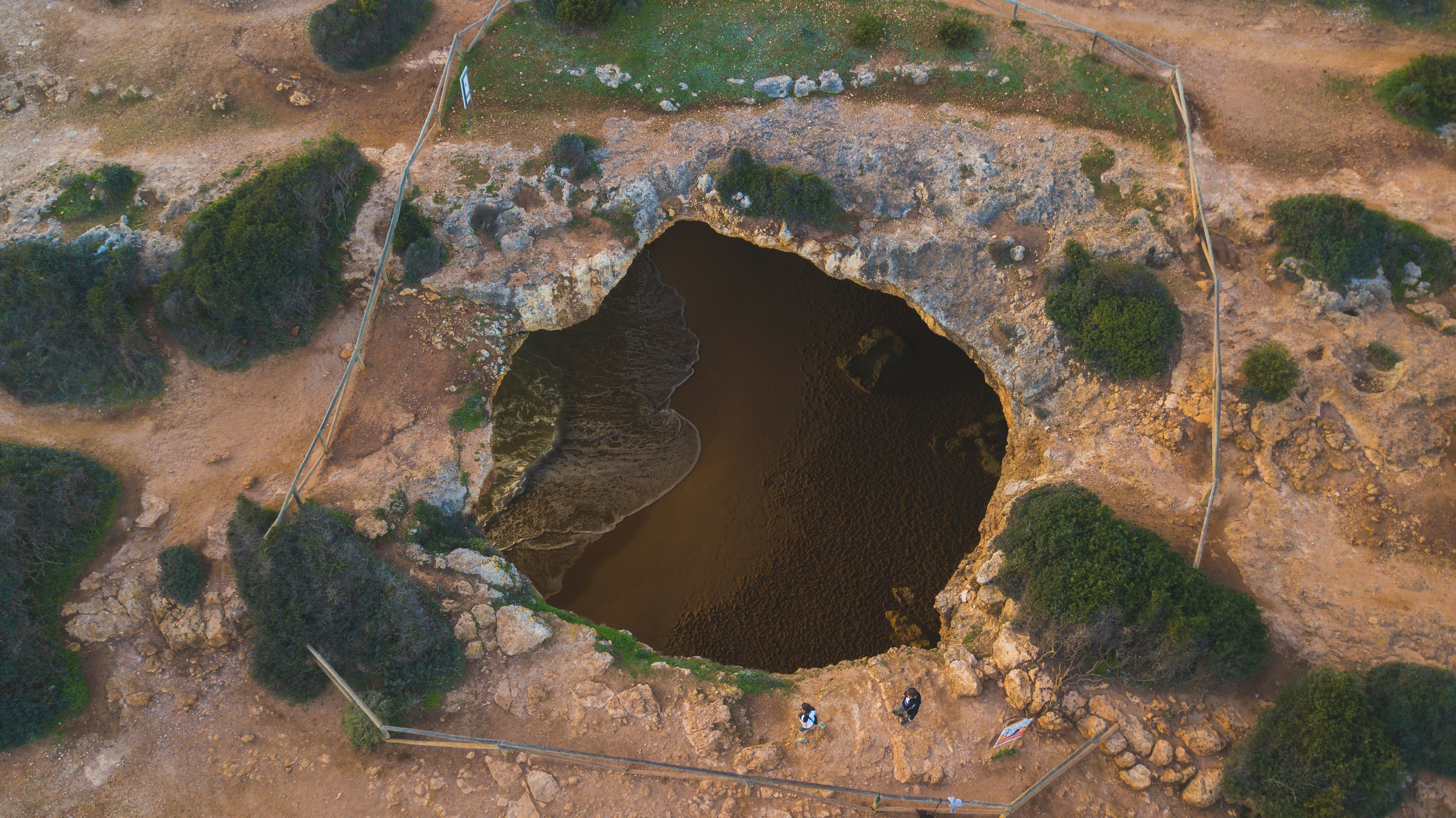 Edge of the Earth: Circular sinkhole framed by a weathered barrier in arid terrain