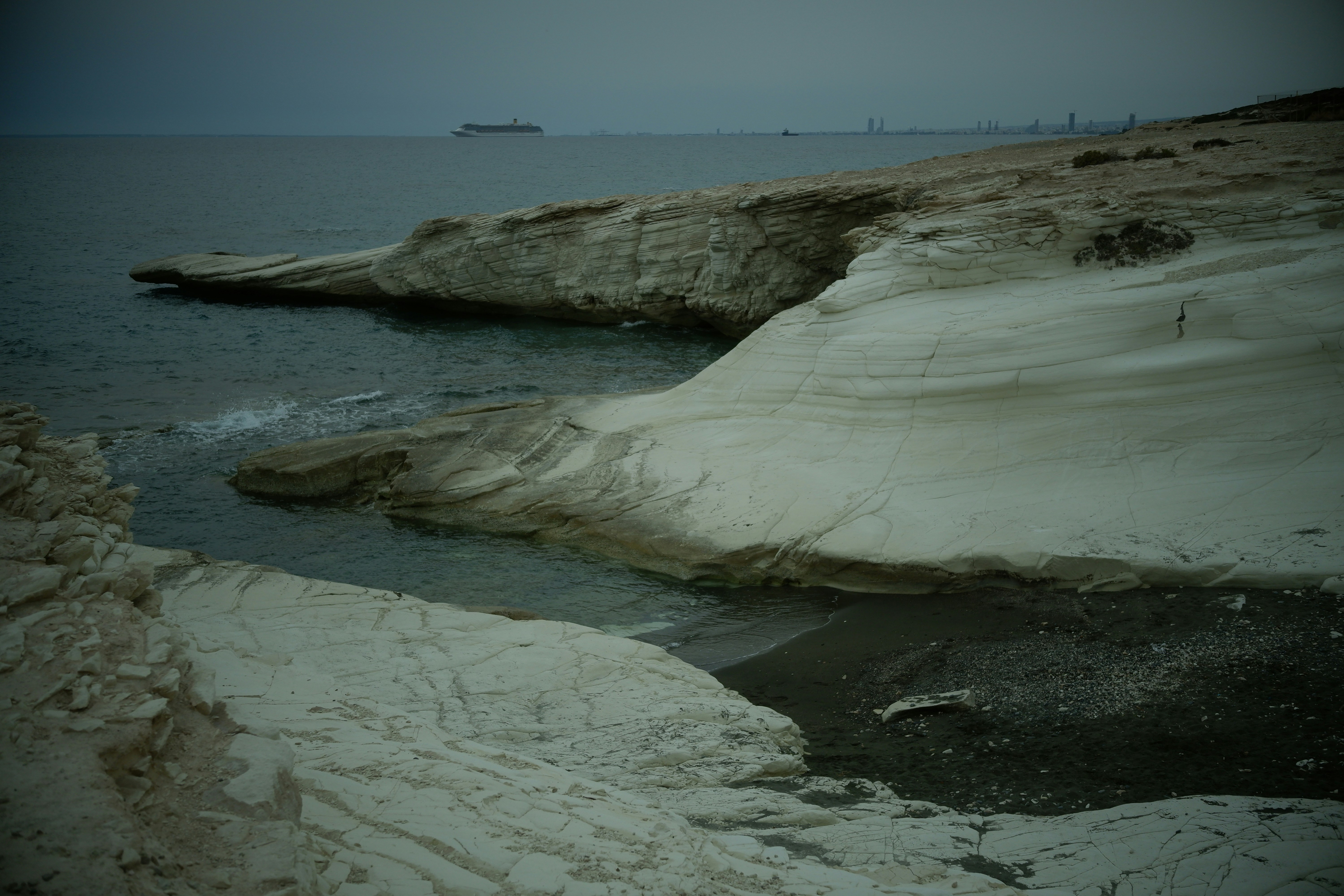 Strata and Sea: White Rock Layers Framing a Distant Vessel