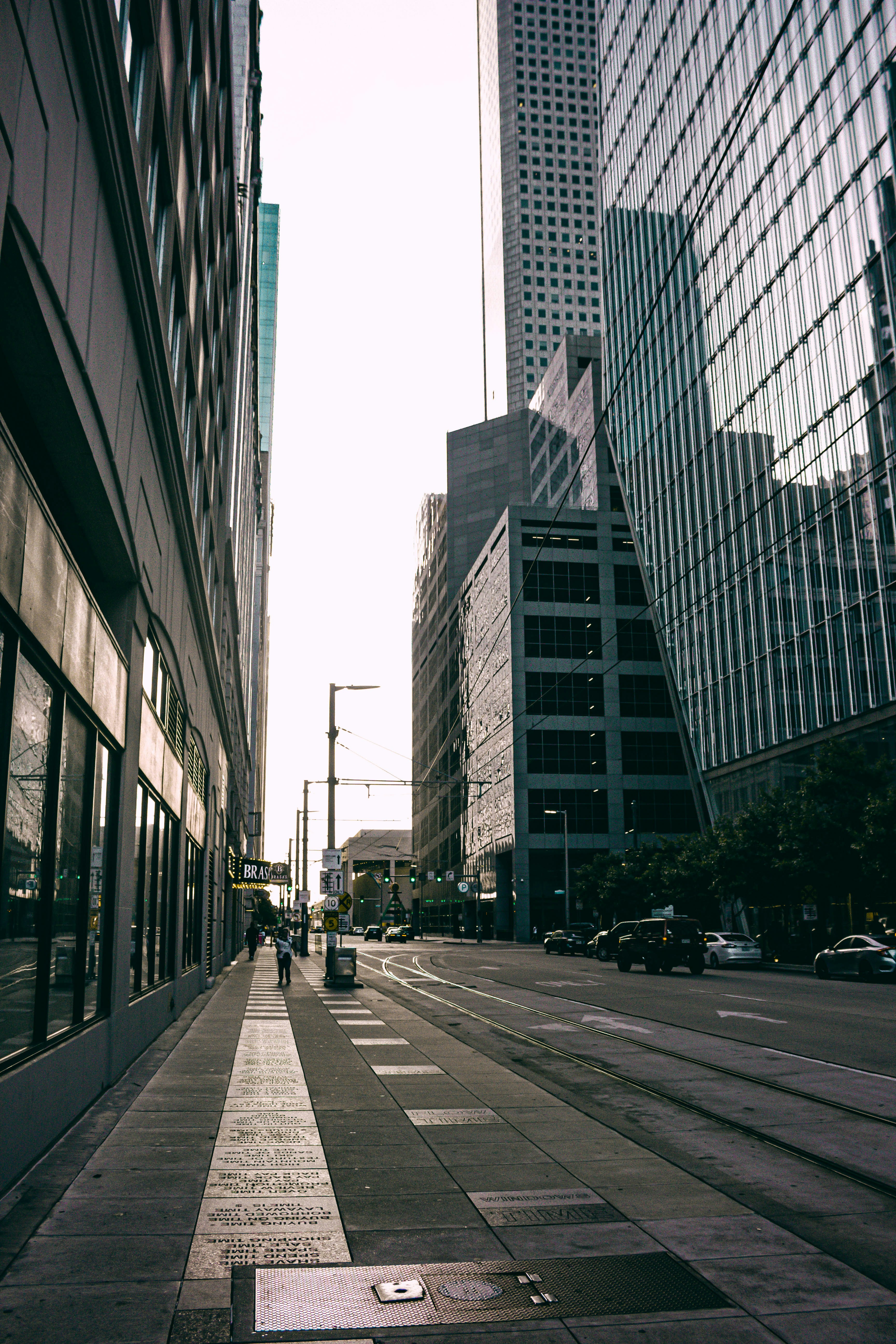 Sunlight filters through towering skyscrapers, casting reflections on the pavement in a bustling city street.