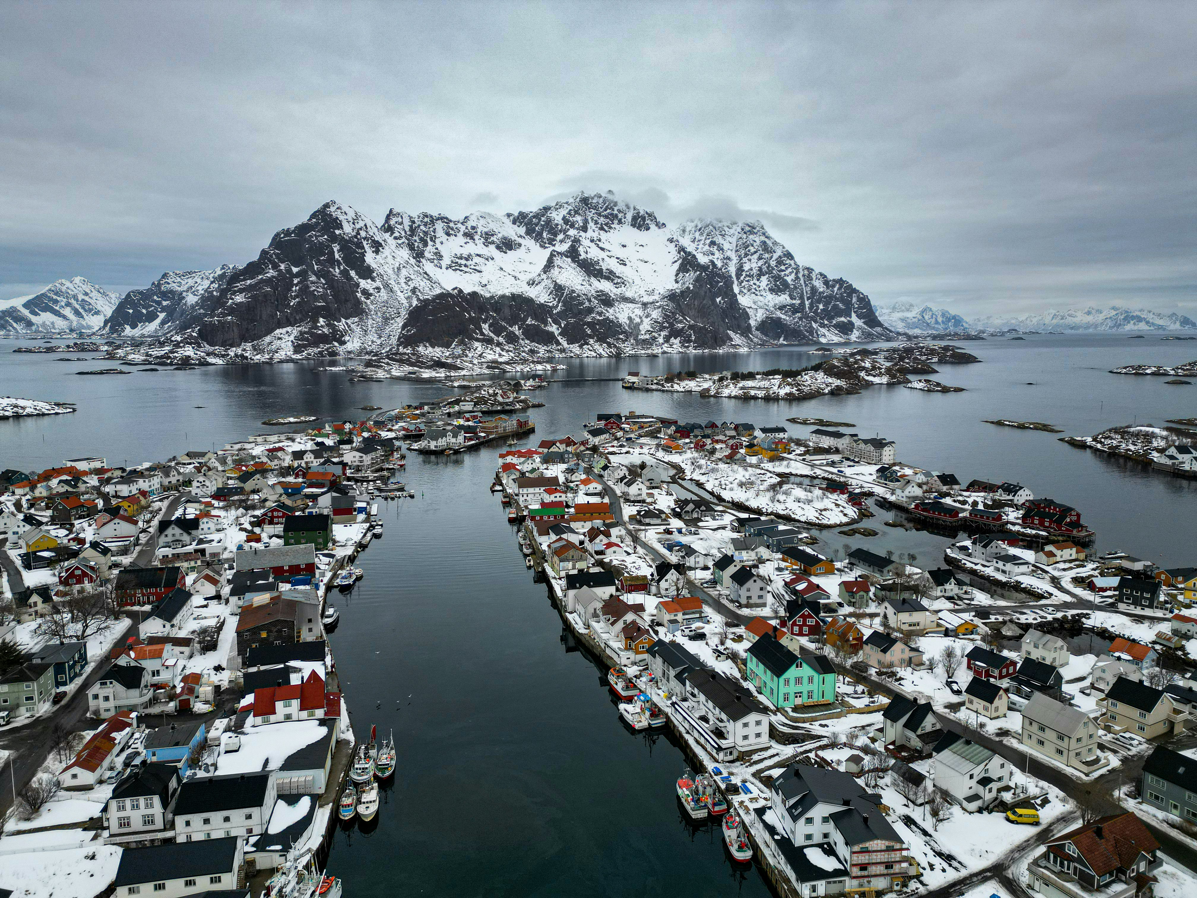 Snow-draped fishing village with colorful houses against towering mountains in Lofoten, Norway.