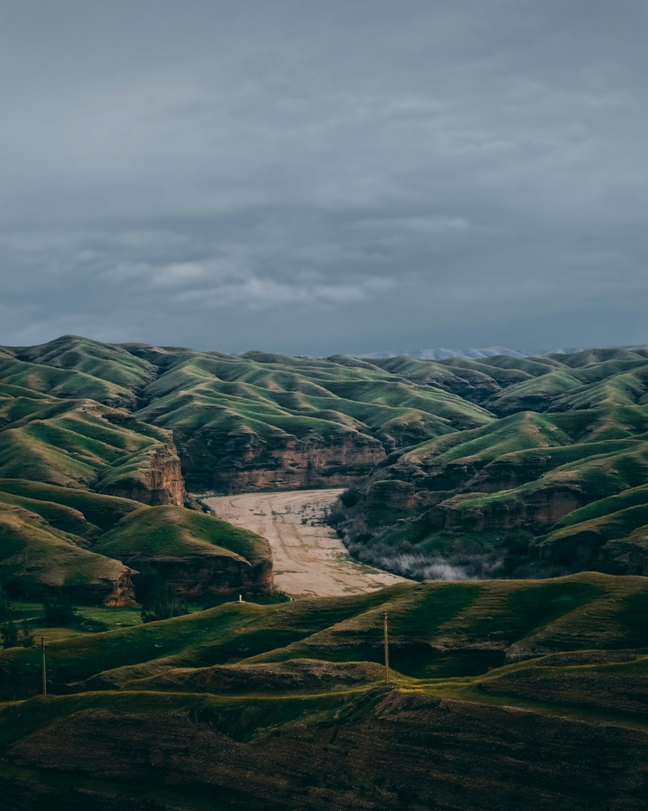 Erosion-carved valley winds through emerald hills under a moody grey sky