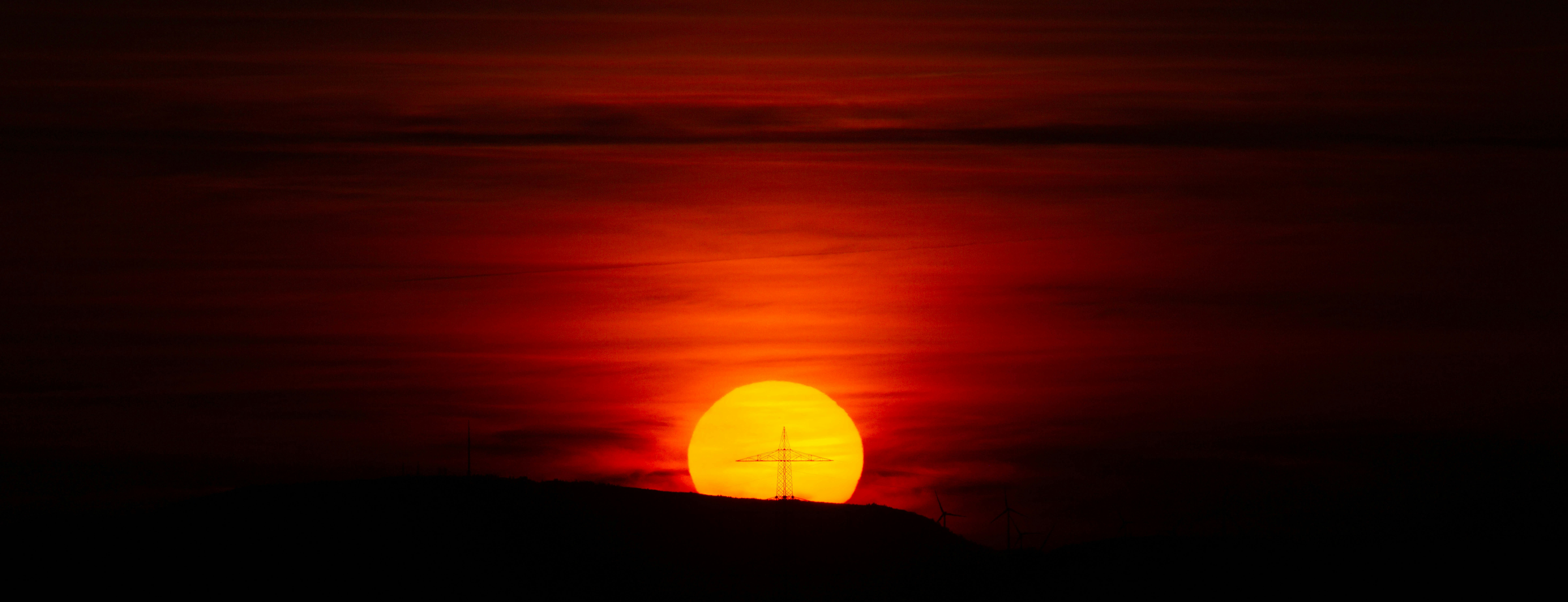 The sun is setting over a hill with a cross in the foreground photo ...