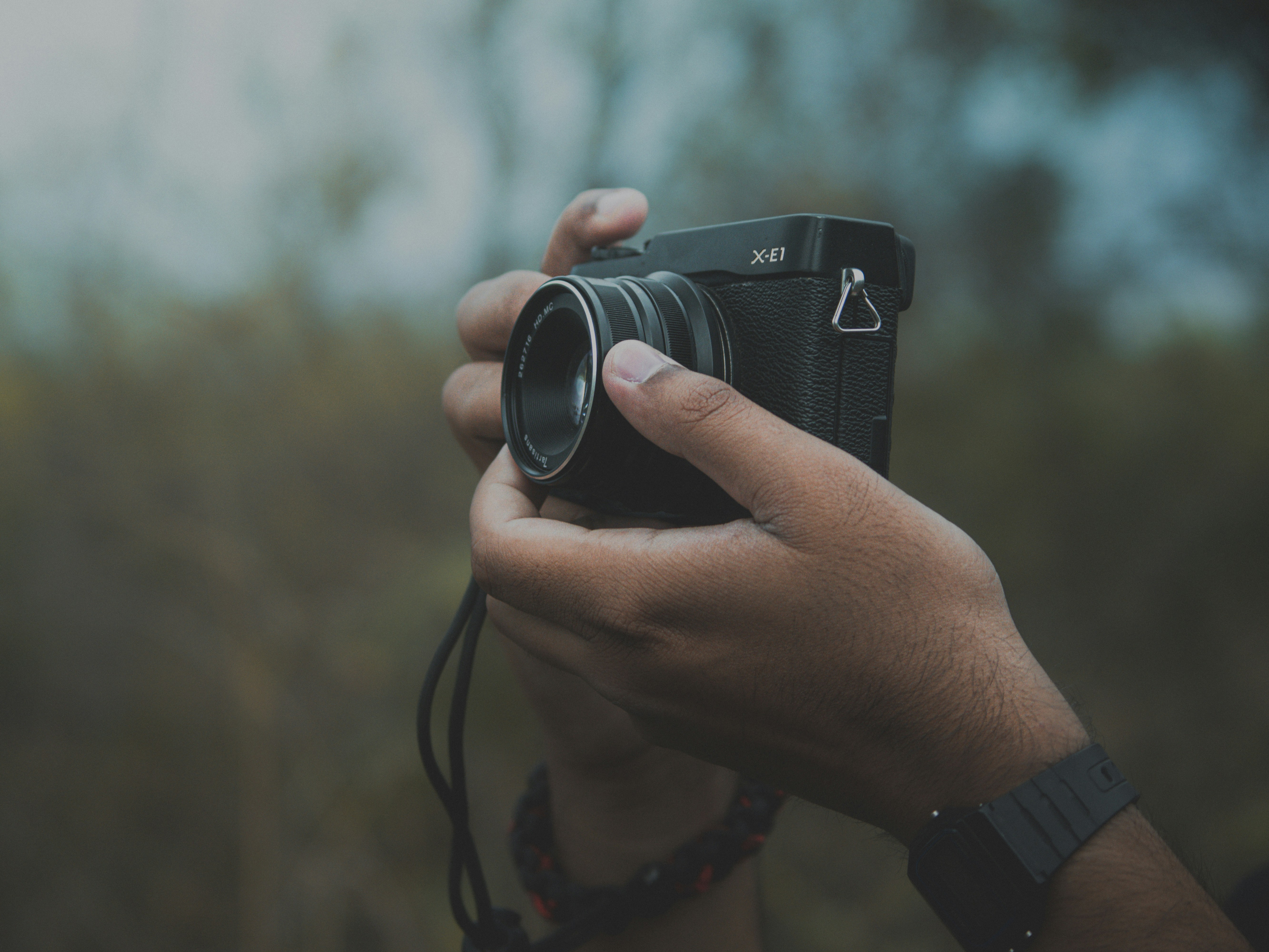 Hands gripping a sleek camera against a blurred natural backdrop, emphasizing the connection between the photographer and their craft.