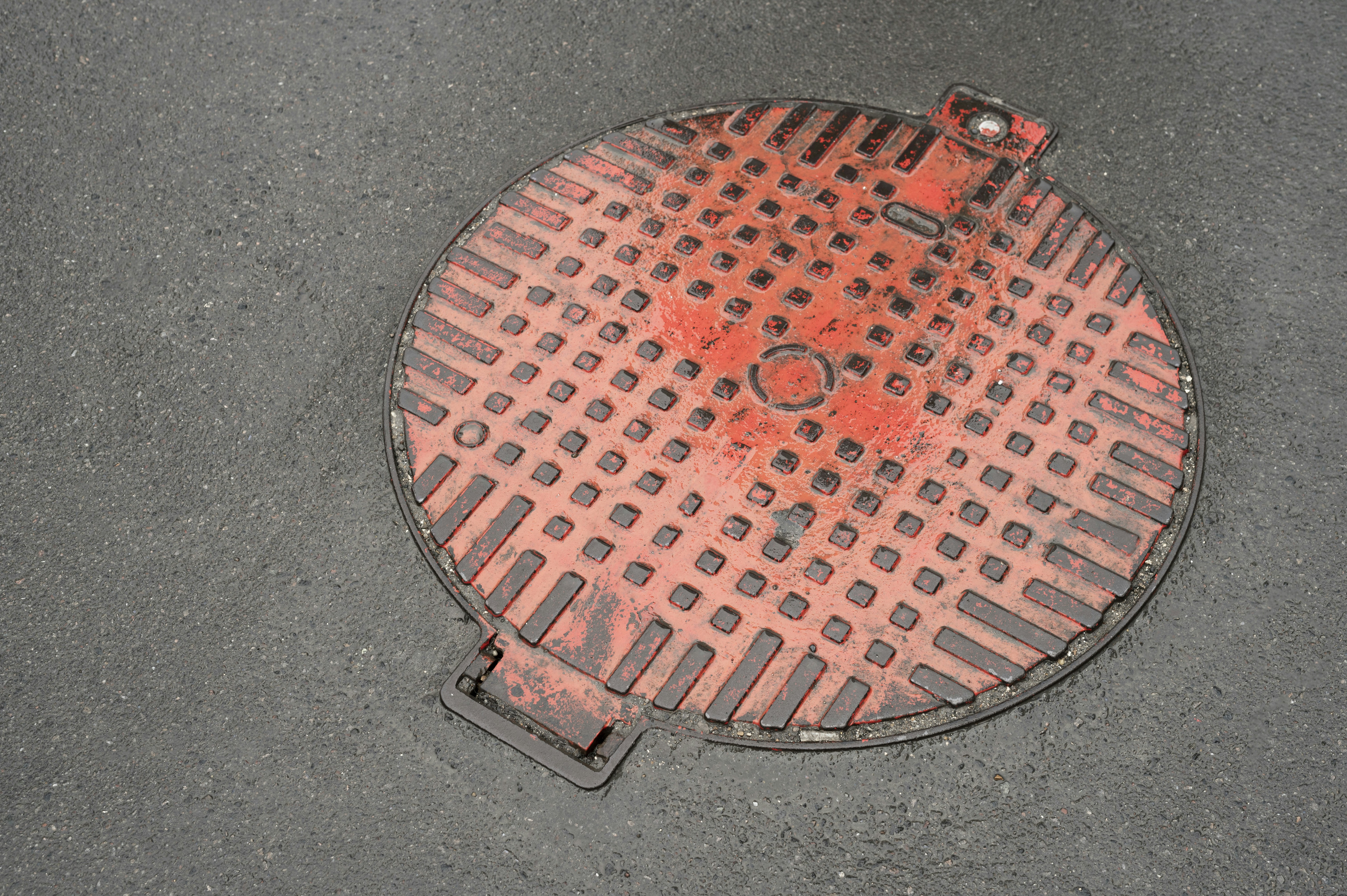 A manhole cover on the ground that is red photo – Free Hole Image on ...