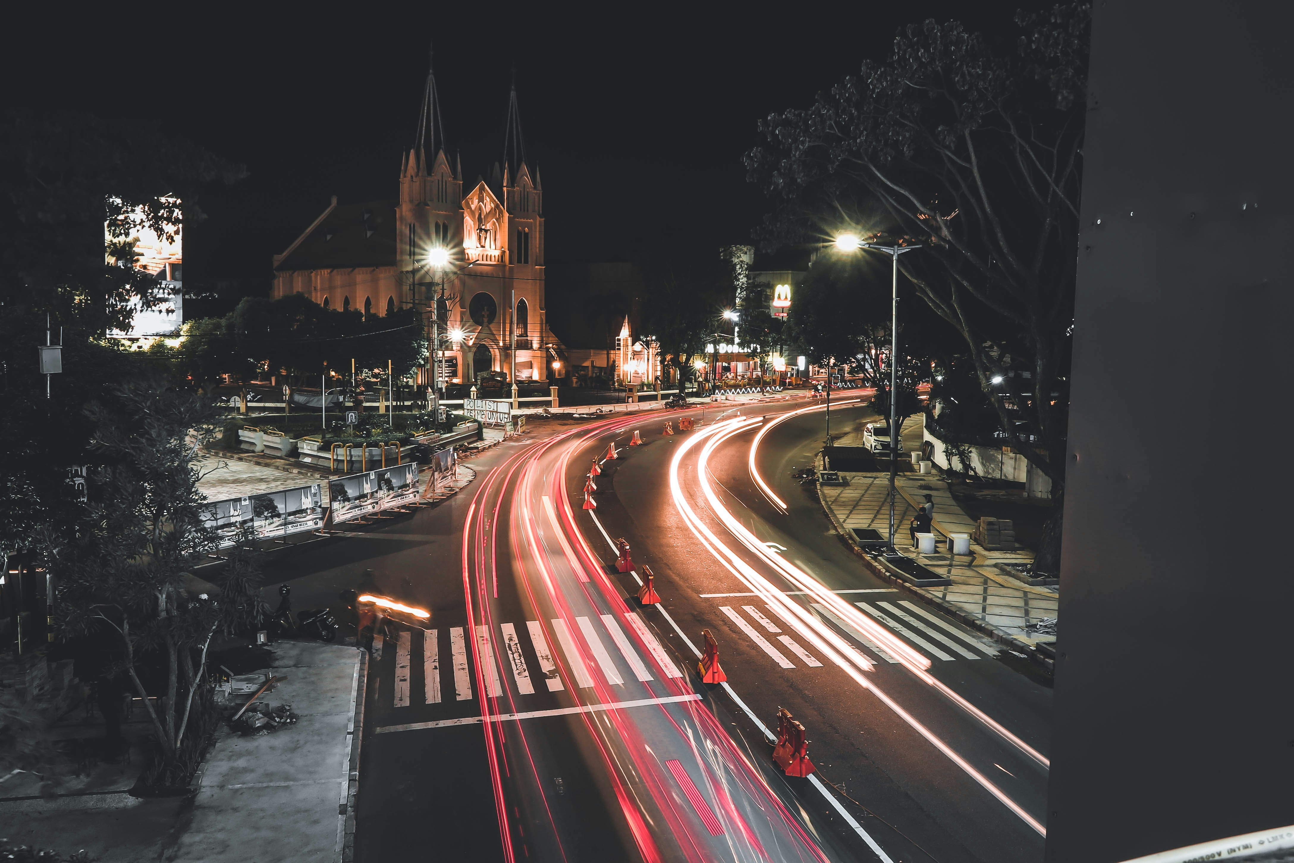 Long exposure shot capturing the dynamic light trails of vehicles along a city street at night, with a historic church in the background.
