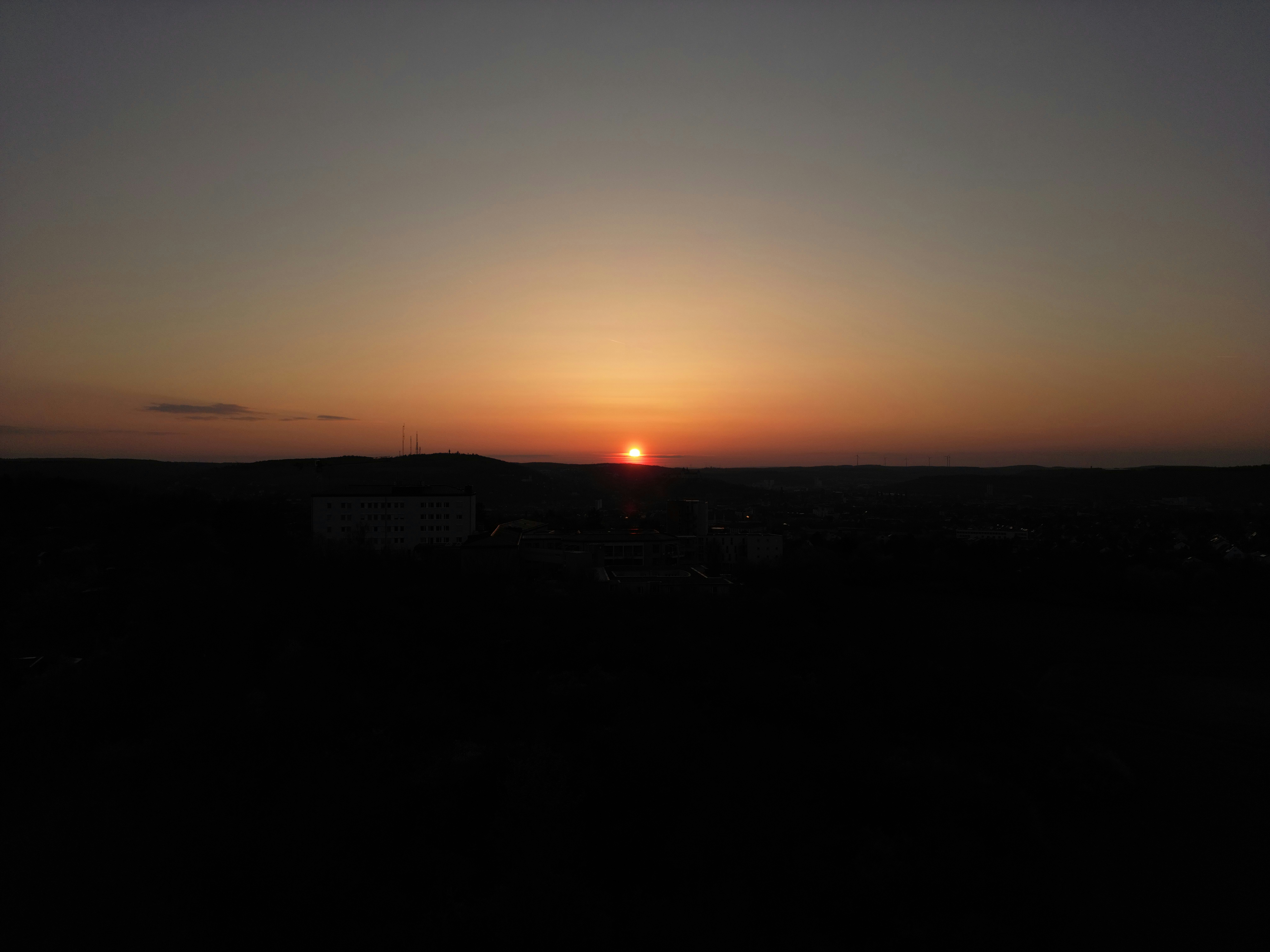 Sun peeking above a dark horizon at dawn with a faint glow in the sky.