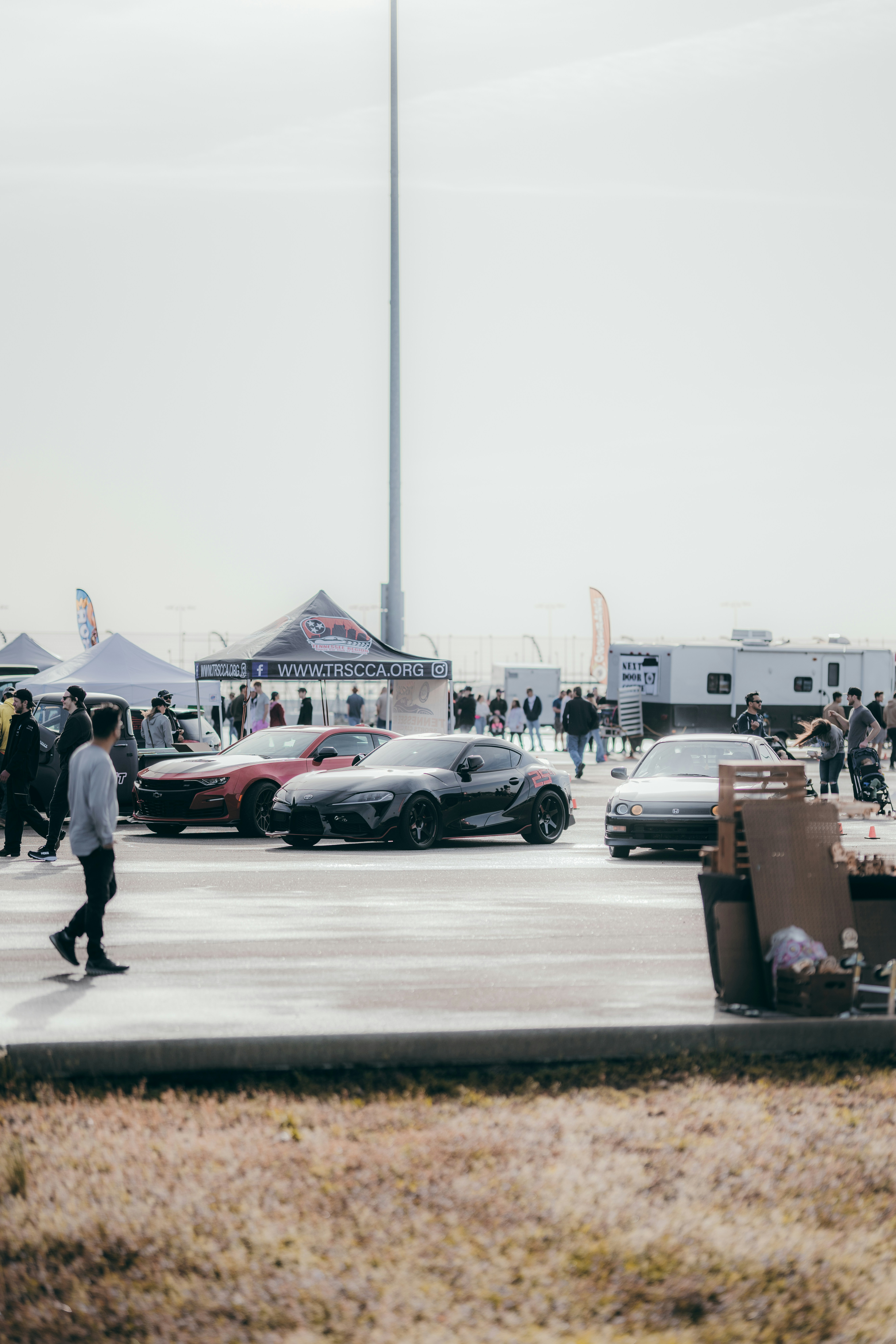 Centerstage at a Sunlit Car Show: The Black Sports Car Among the Tents