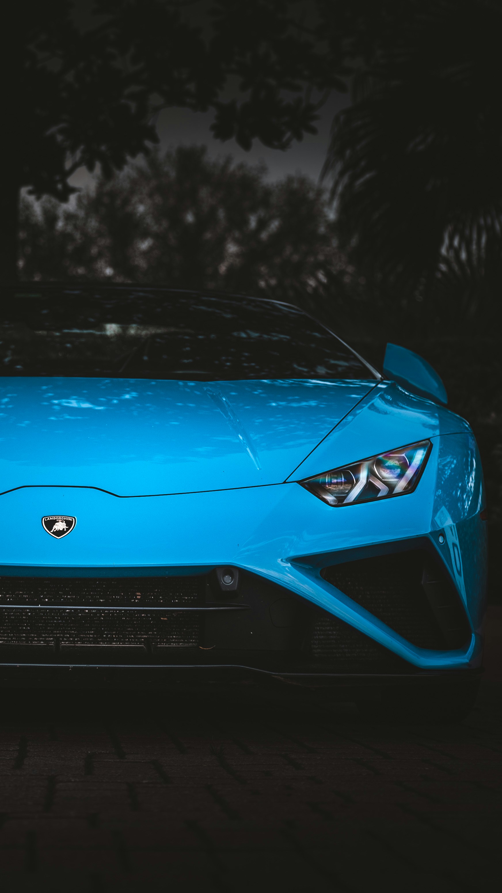 Close-up view of a striking blue Lamborghini sports car showcasing its aerodynamic design and intricate details. The dark background enhances the car's vibrant color.