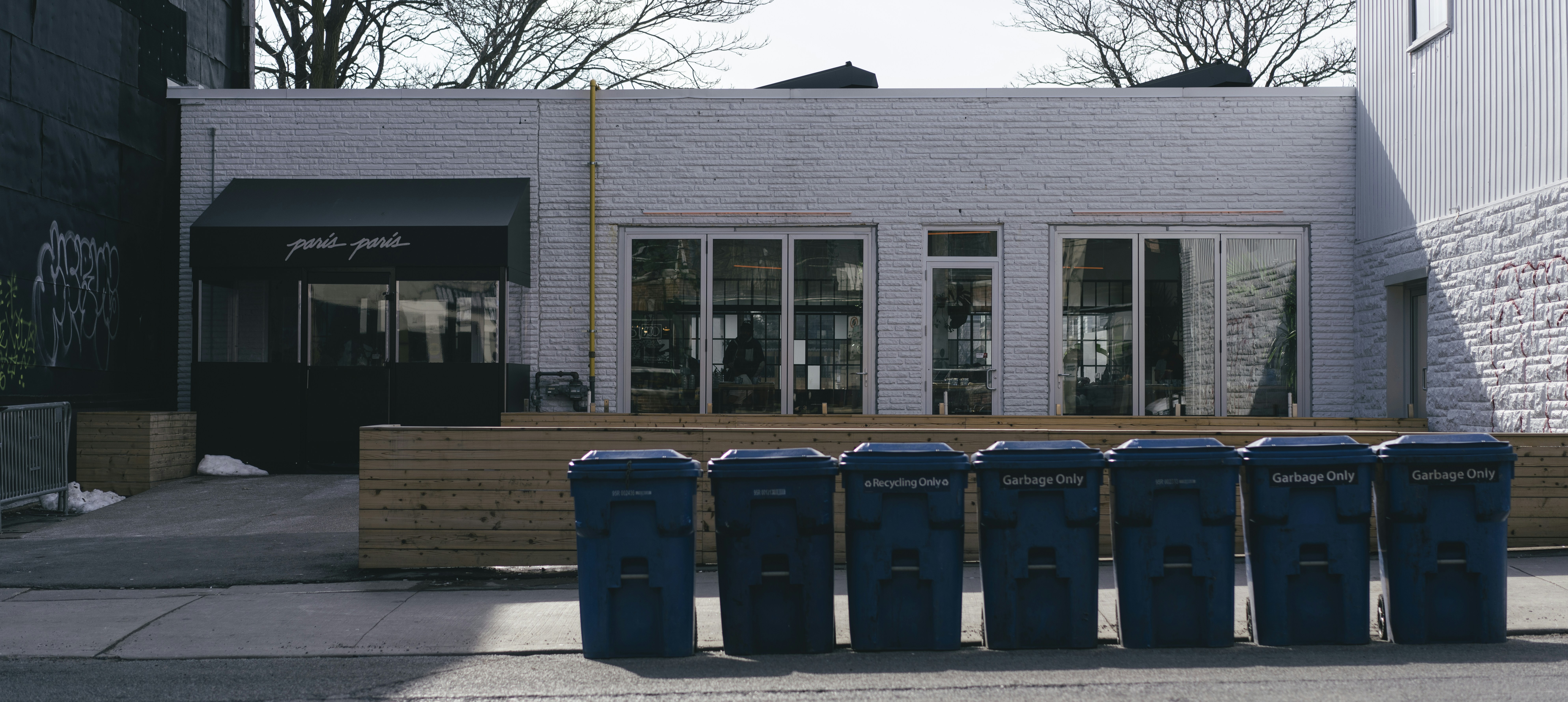A row of blue trash cans sitting in front of a building photo – Free ...