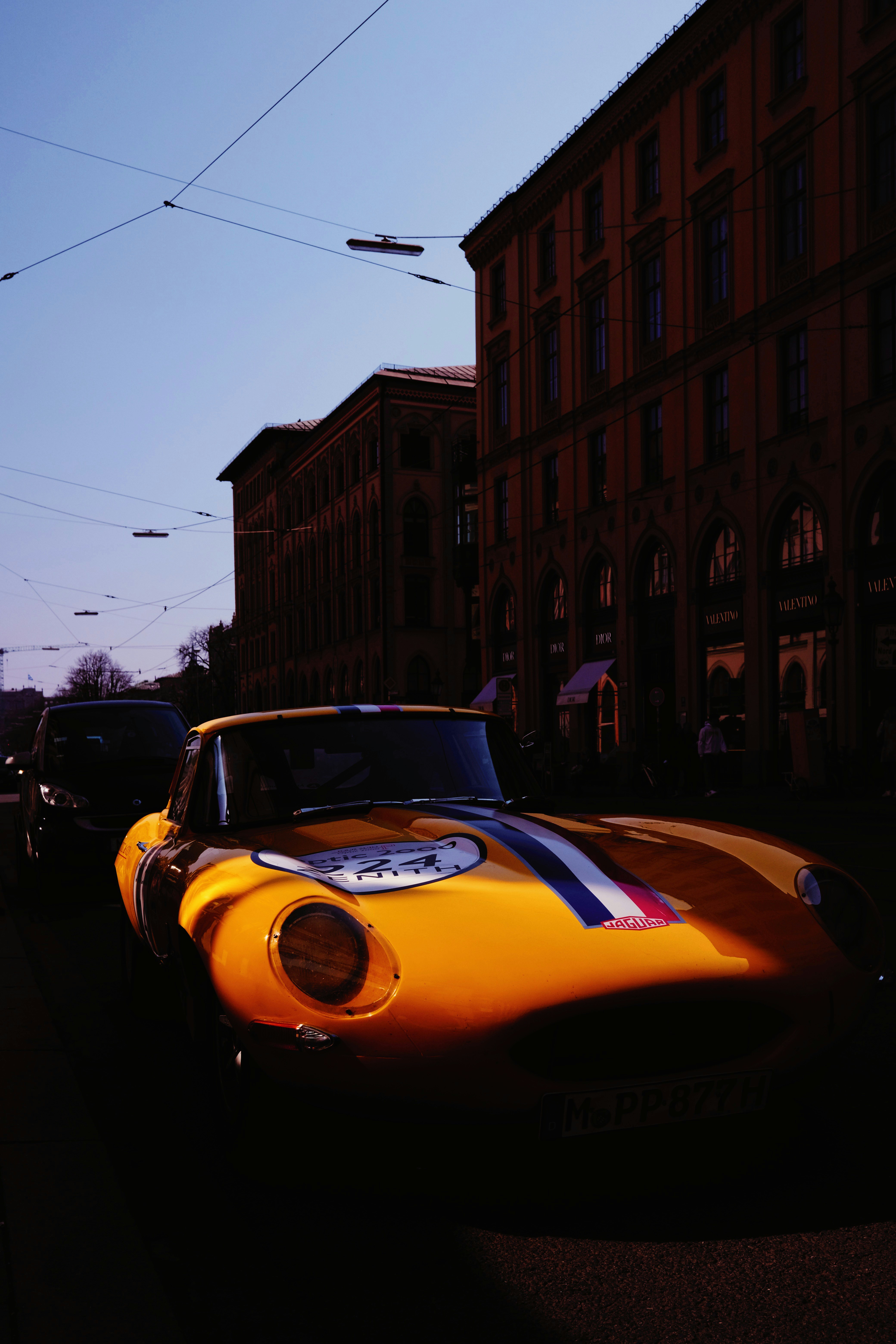 Sunlit Vintage Racer on a Narrow City Street Beneath Tram Wires