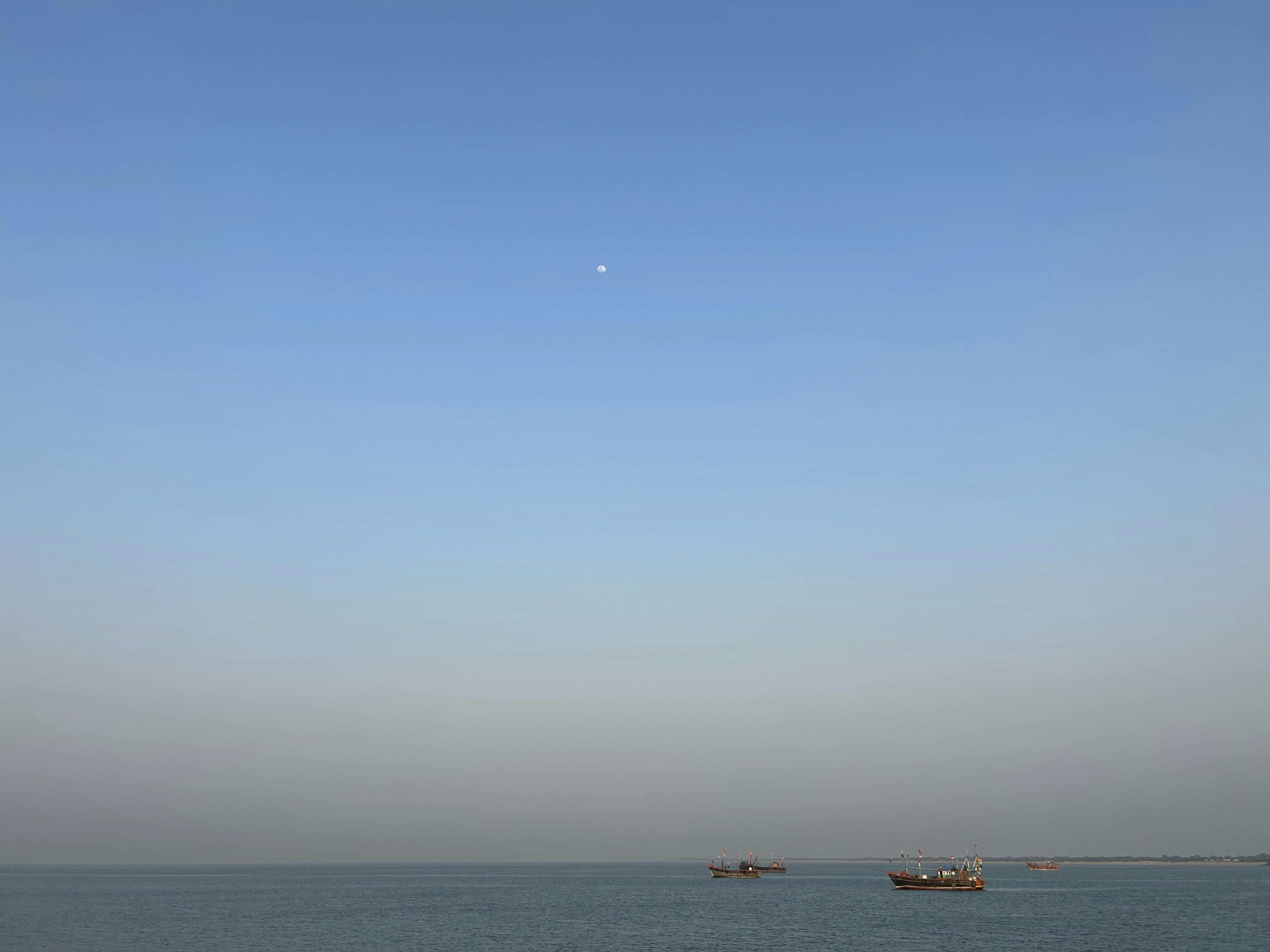 Tranquil seascape with distant boats under a vast blue sky.