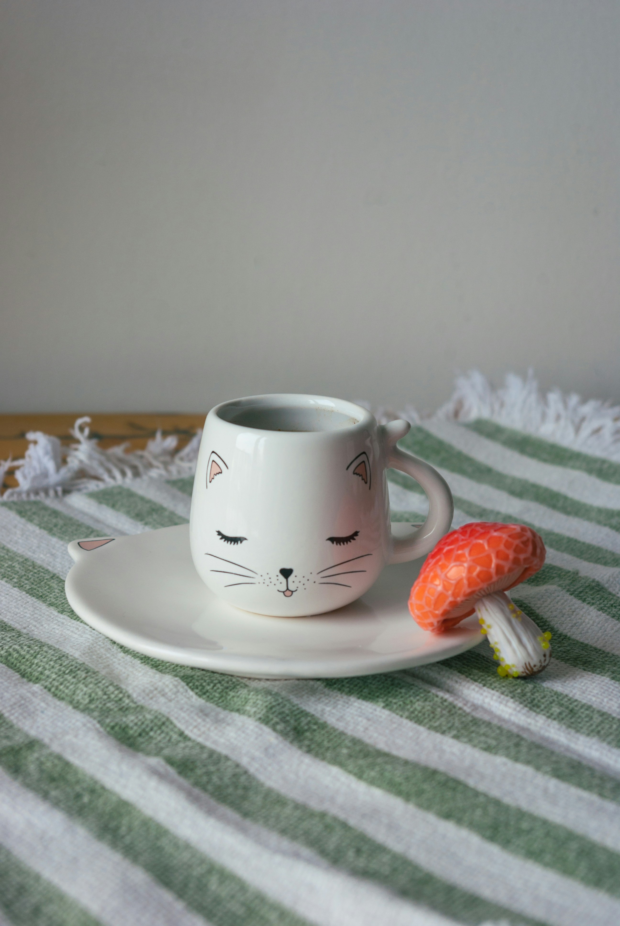Whiskered Morning: Cat-Face Mug on Striped Cloth with a Bright Mushroom Companion