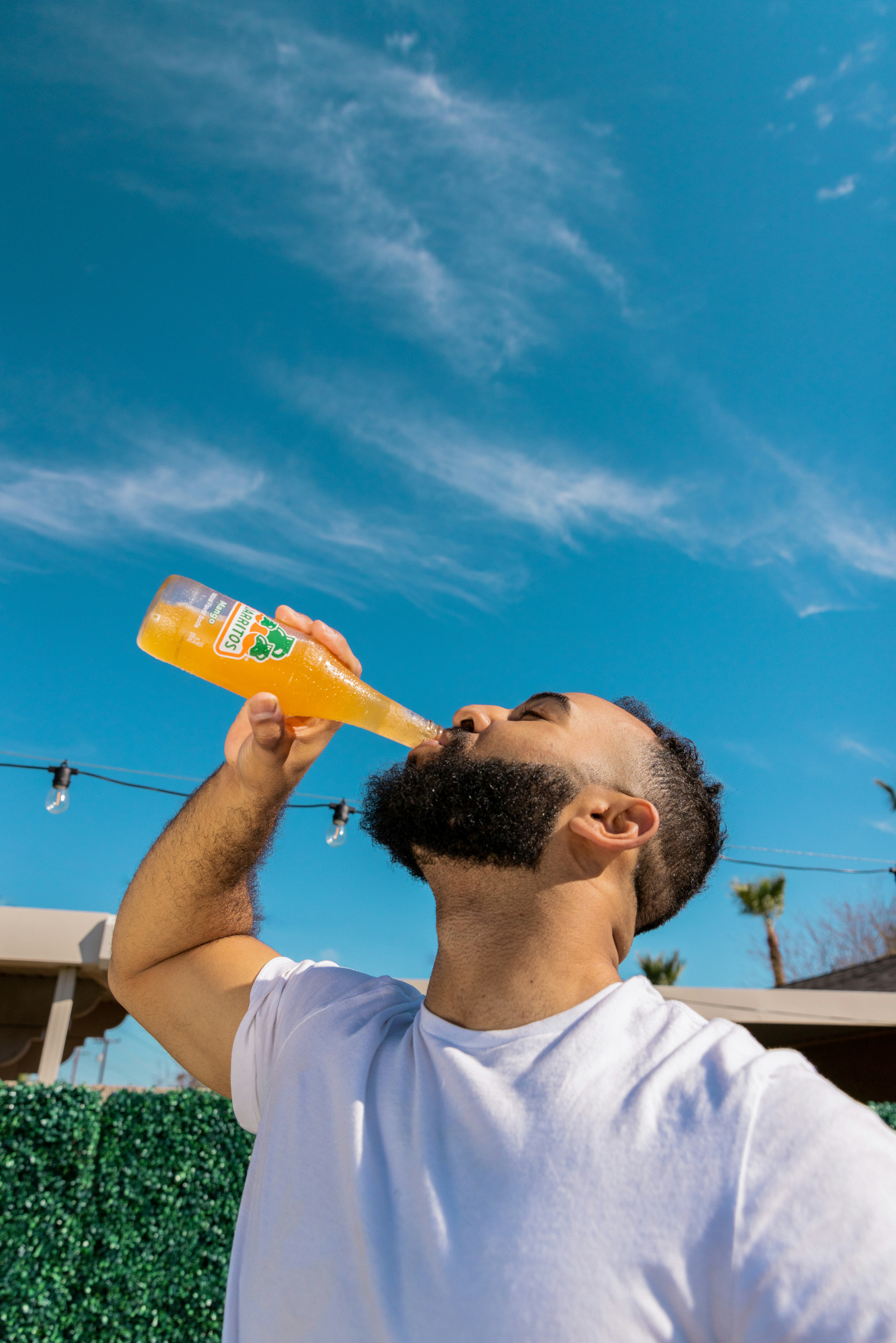 Man enjoying mango Jarritos soda with blue skies while on summer vacation.