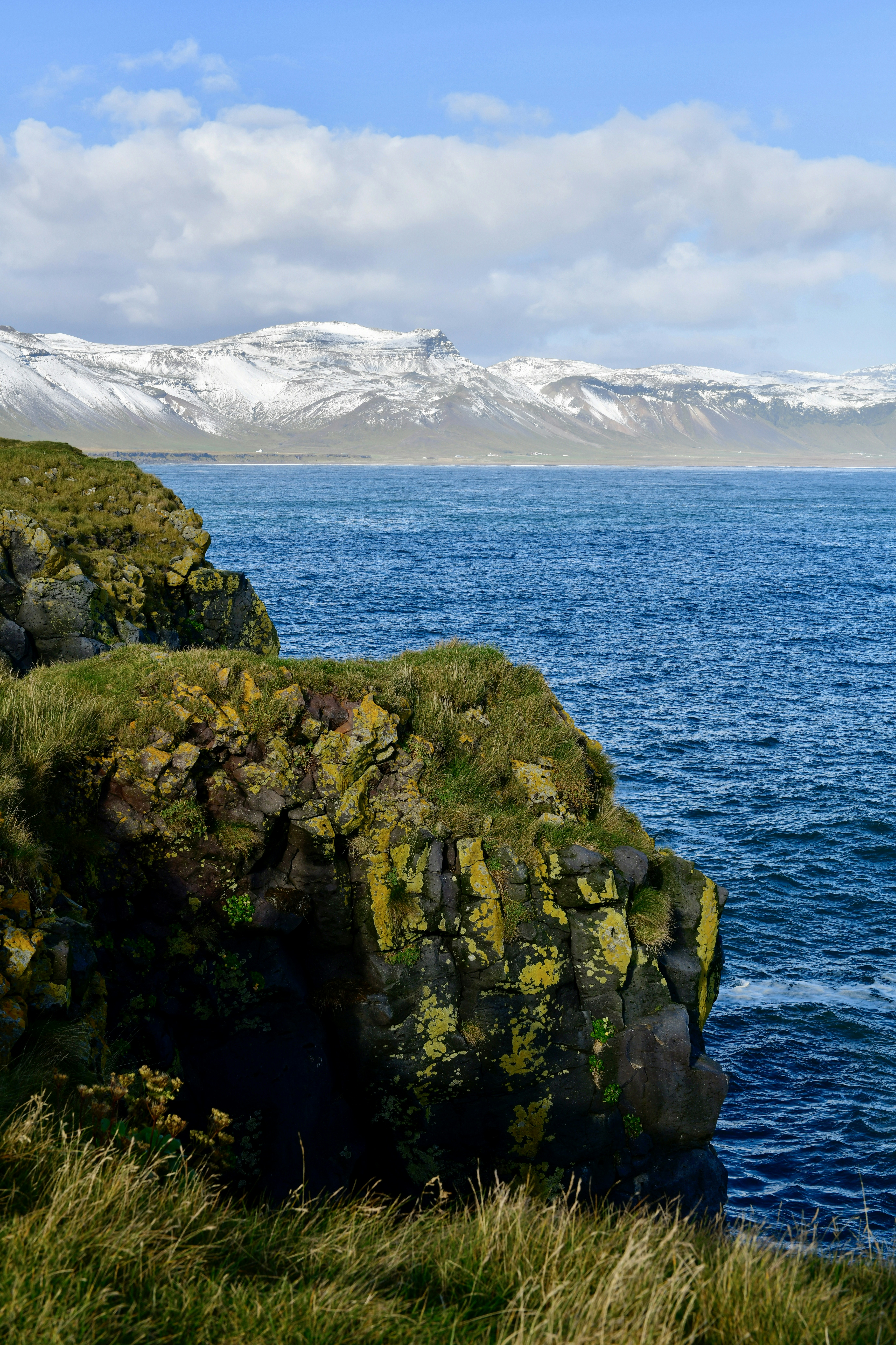 Lichen-Clad Cliffs Over a Deep Atlantic, Snow-Kissed Peaks on the Horizon