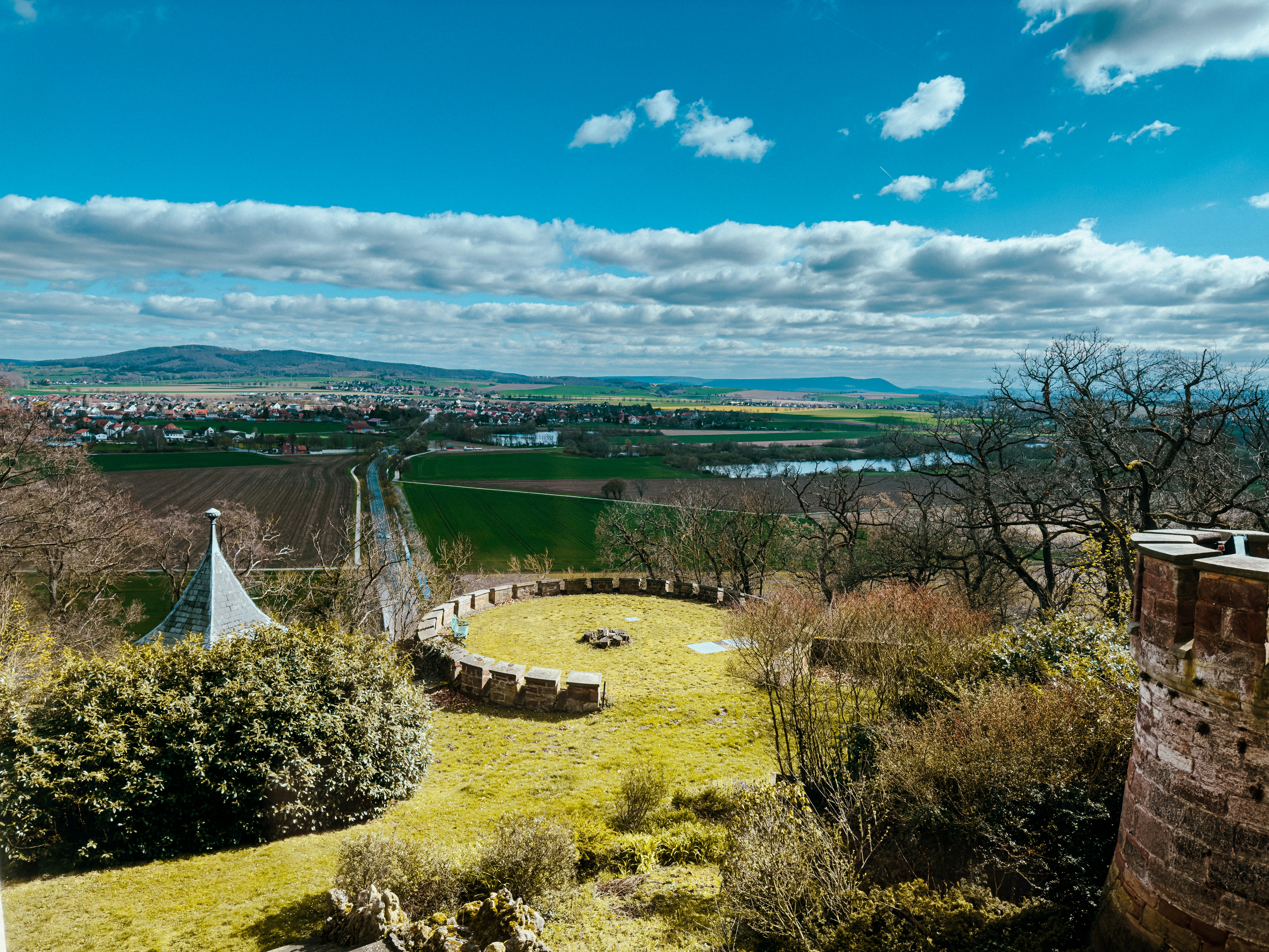 Circular stone seating area in a lush garden with distant rolling hills under a vivid blue sky.