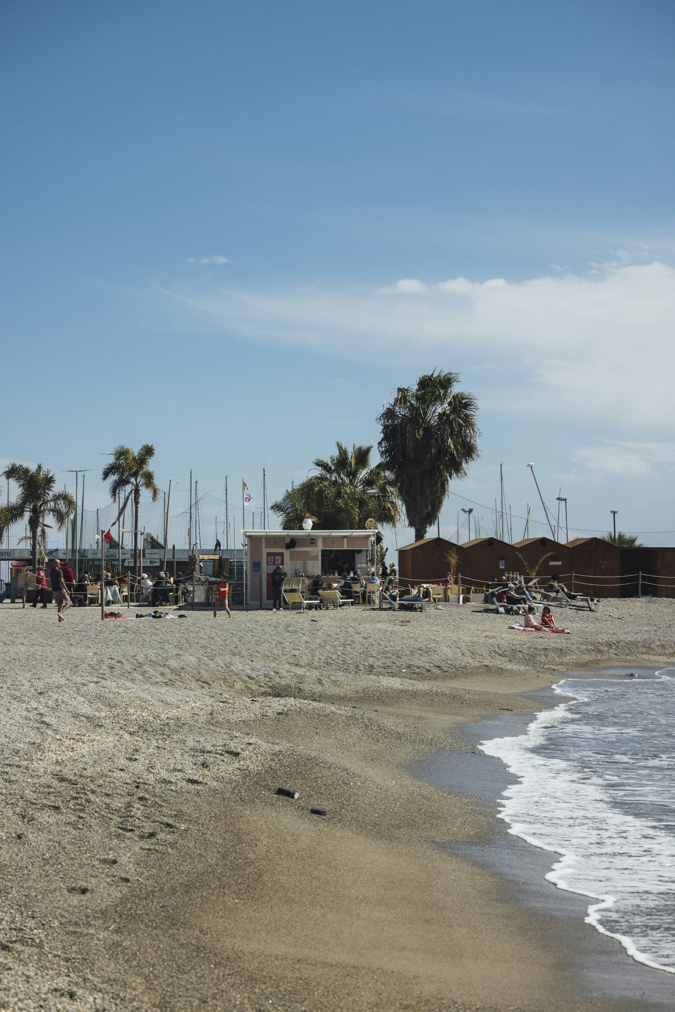 Palm-lined Beachfront at Dusk: Beachgoers and Boats in Quiet Harbor