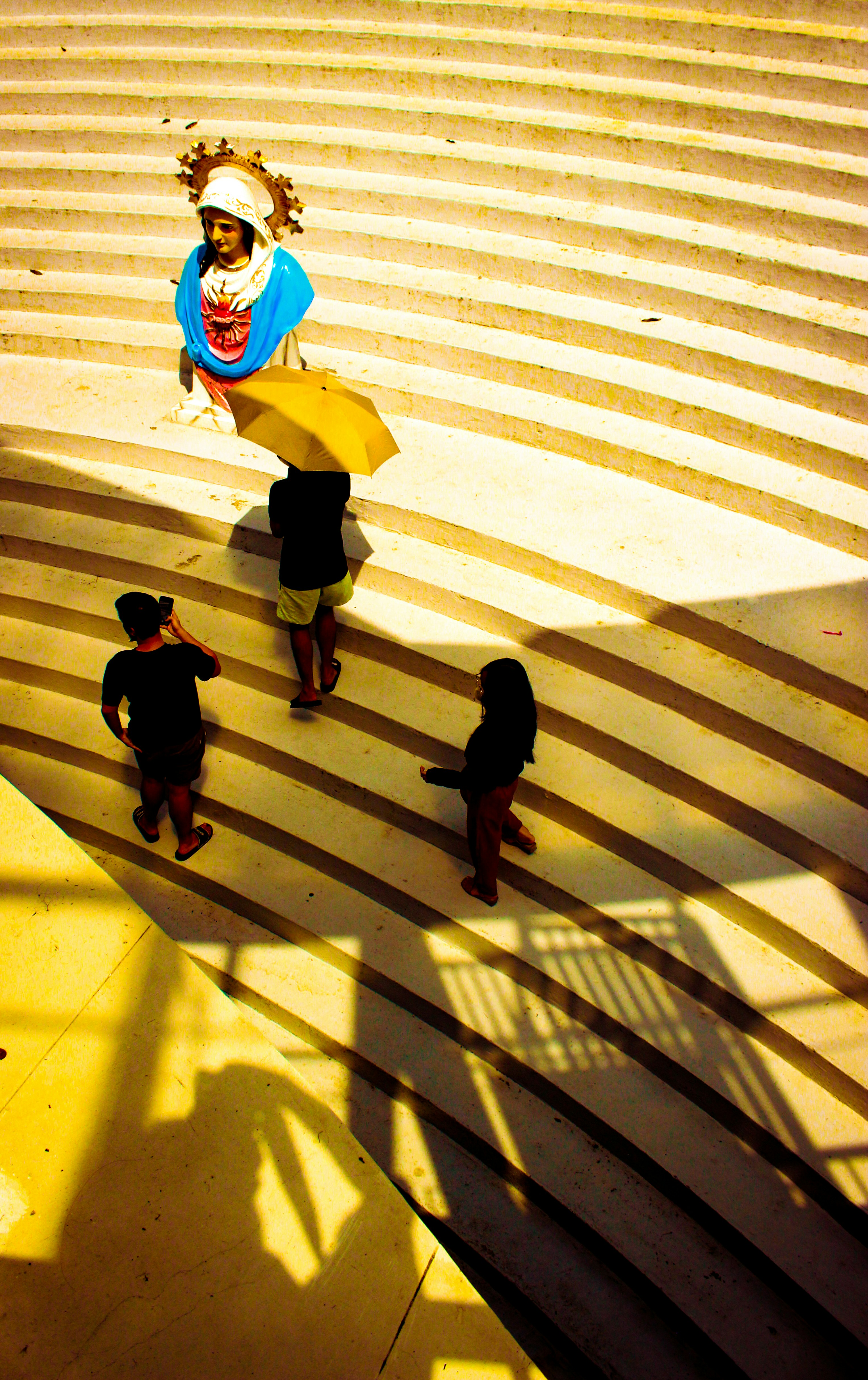 A figure adorned in traditional attire stands at the center of a circular staircase, while three individuals interact nearby, creating a dynamic scene of cultural exchange.