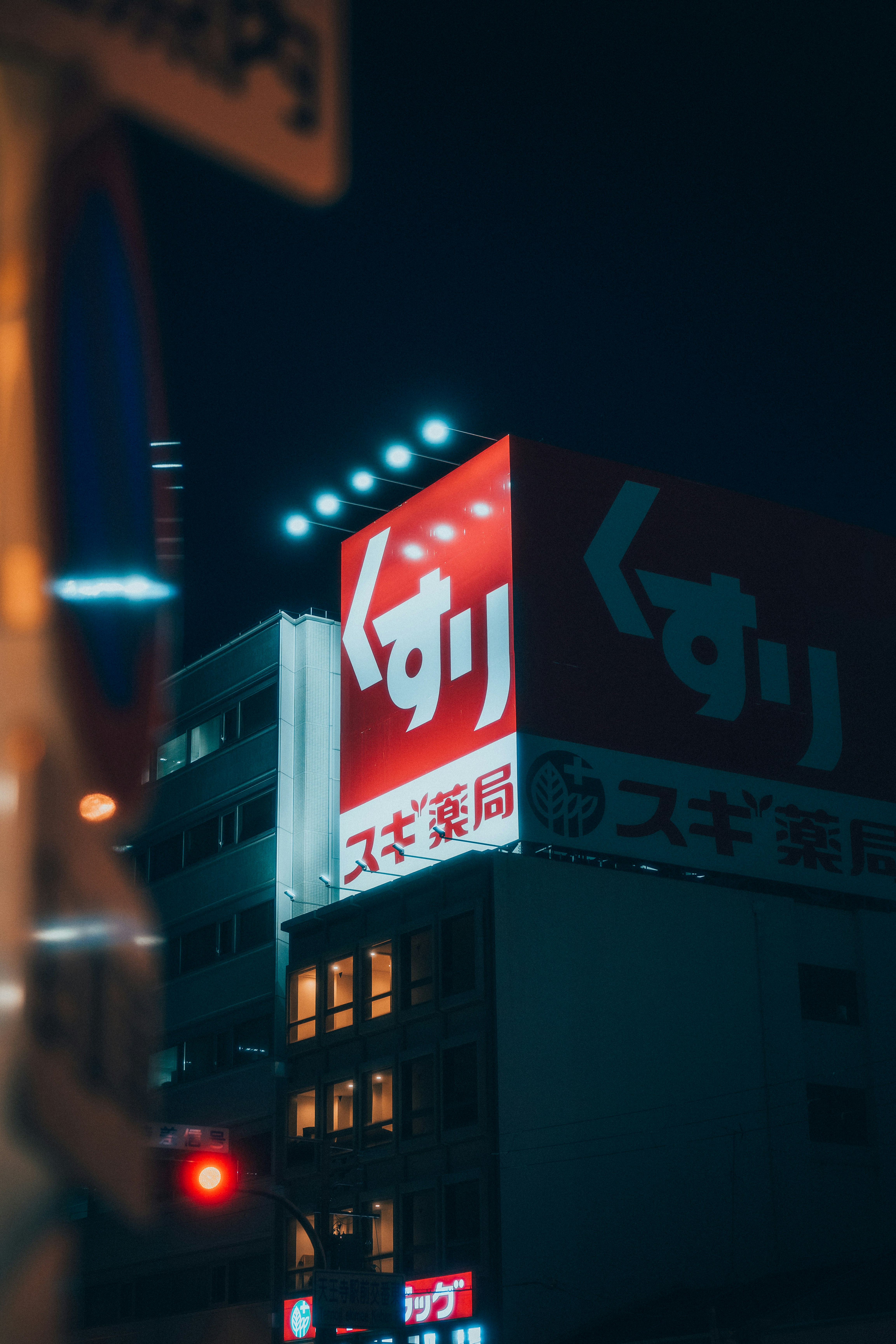Vibrant neon signage illuminating a cityscape at night, showcasing a pharmacy advertisement. The interplay of light and shadow adds depth to the urban environment.