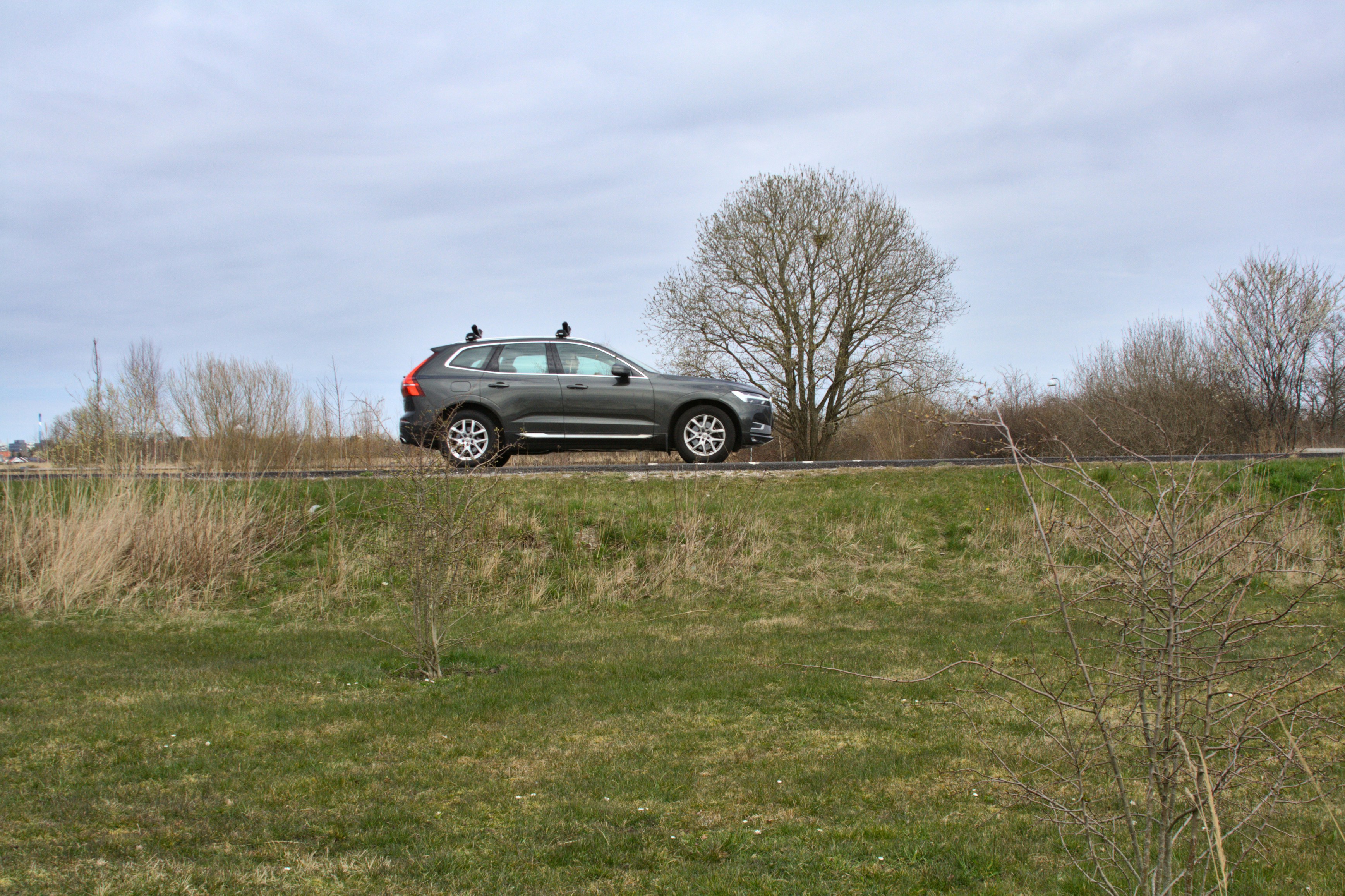 SUV traveling along a rural road bordered by grass and bare trees under an overcast sky.