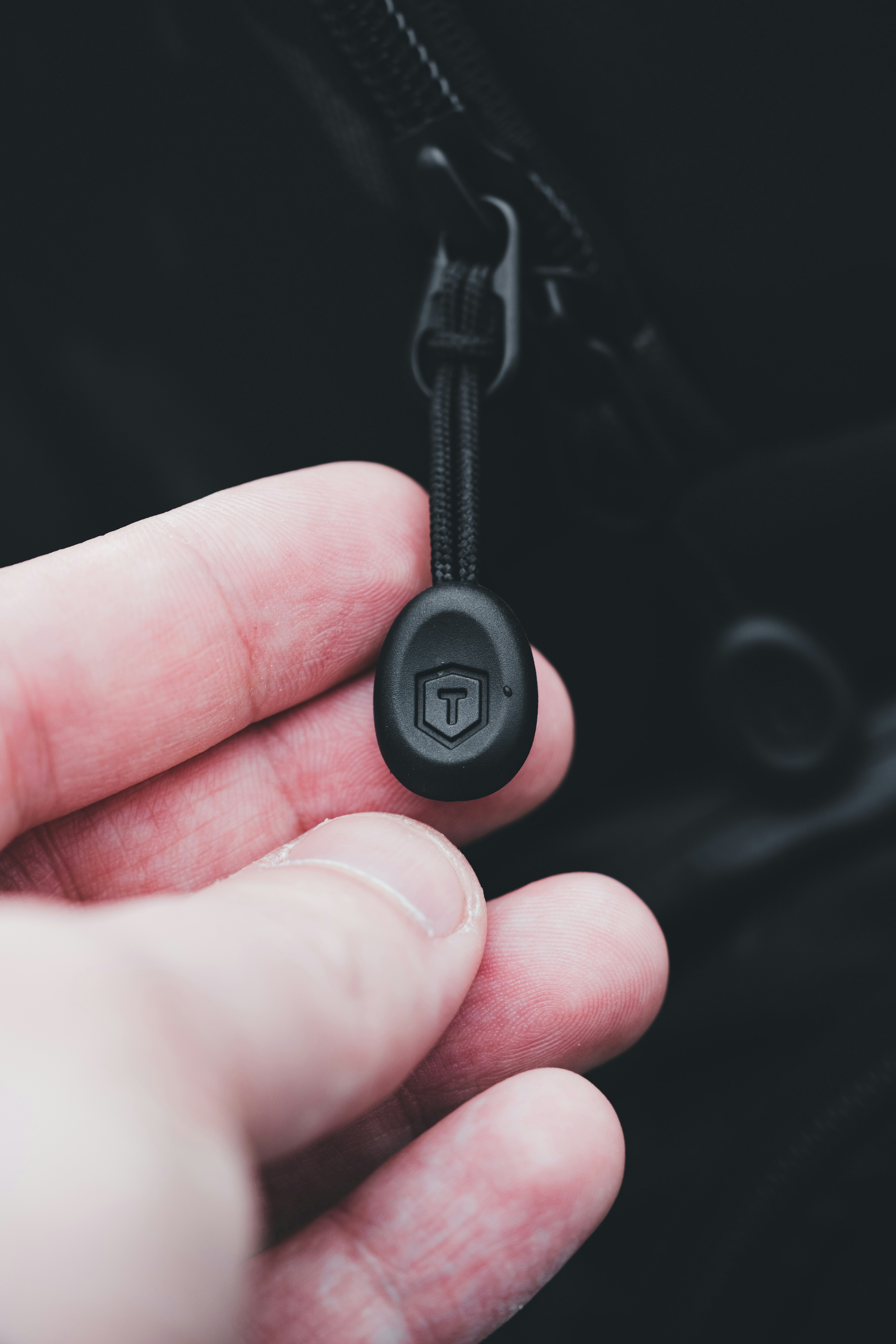 T-Logo Close-Up: A Zipper Pull Portrait on Dark Fabric