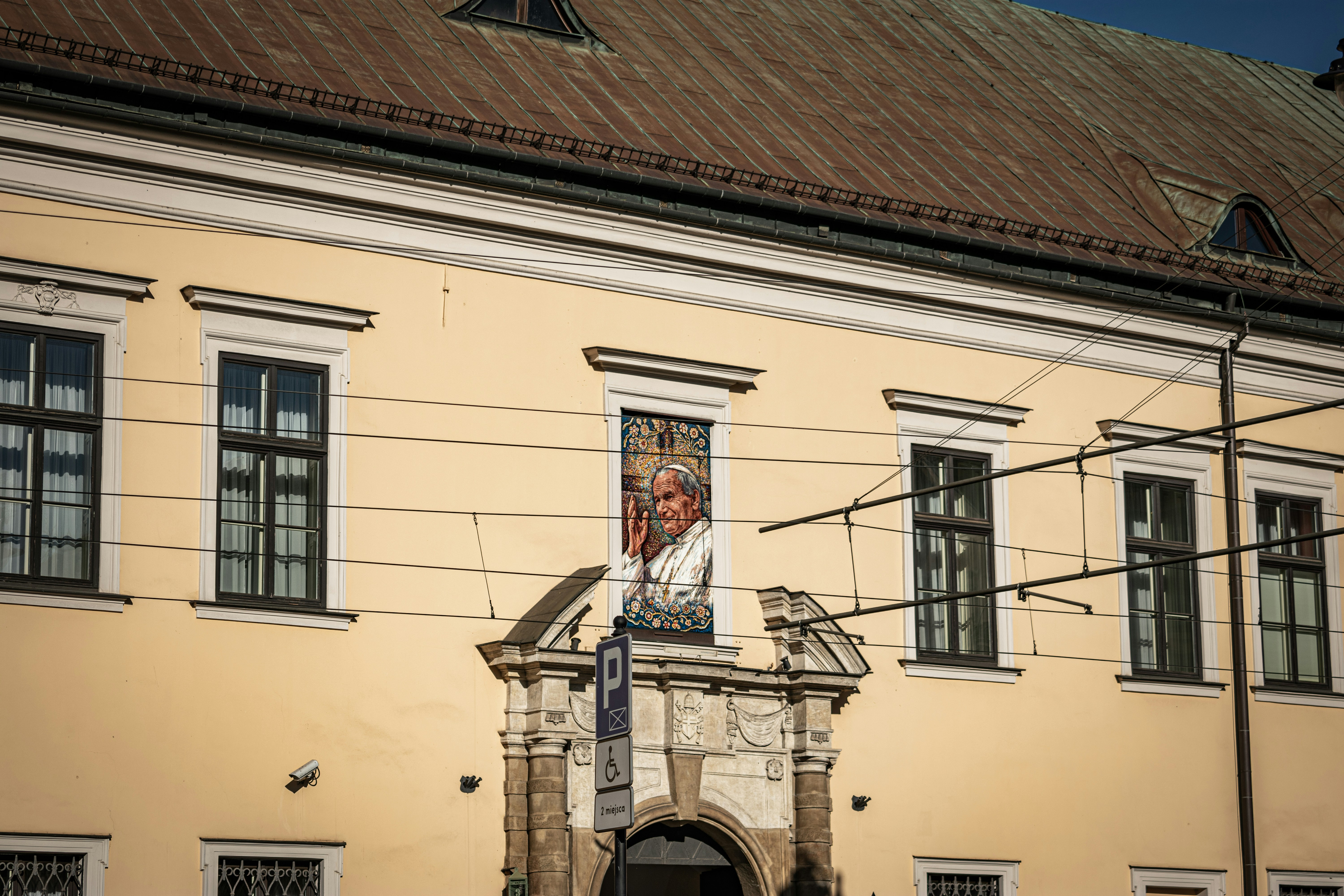 A mural of a serene figure in prayer adorns the facade of a historic building, framed by architectural details and urban elements.