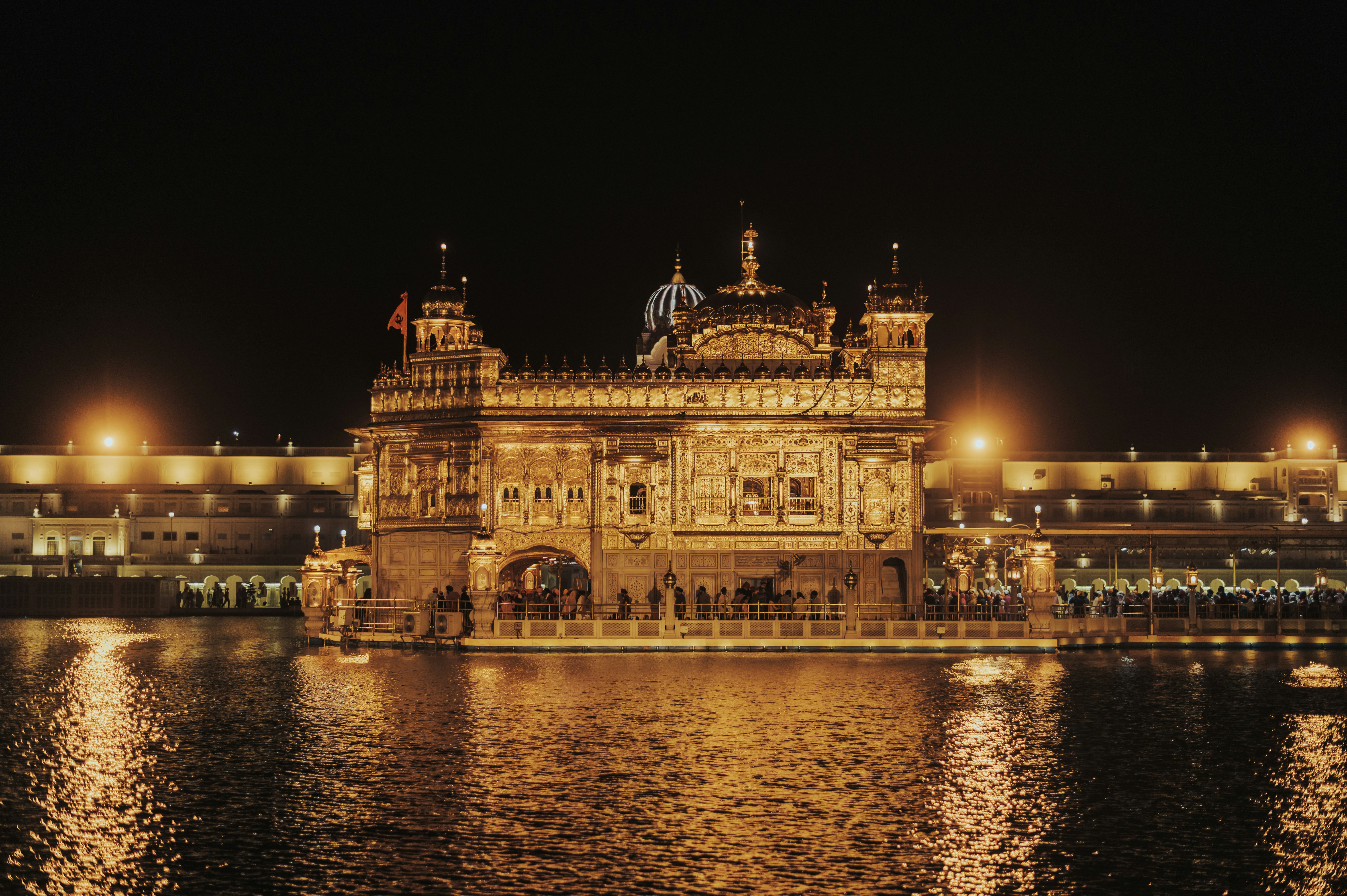 Golden temple illuminated at night, reflecting on a serene body of water.