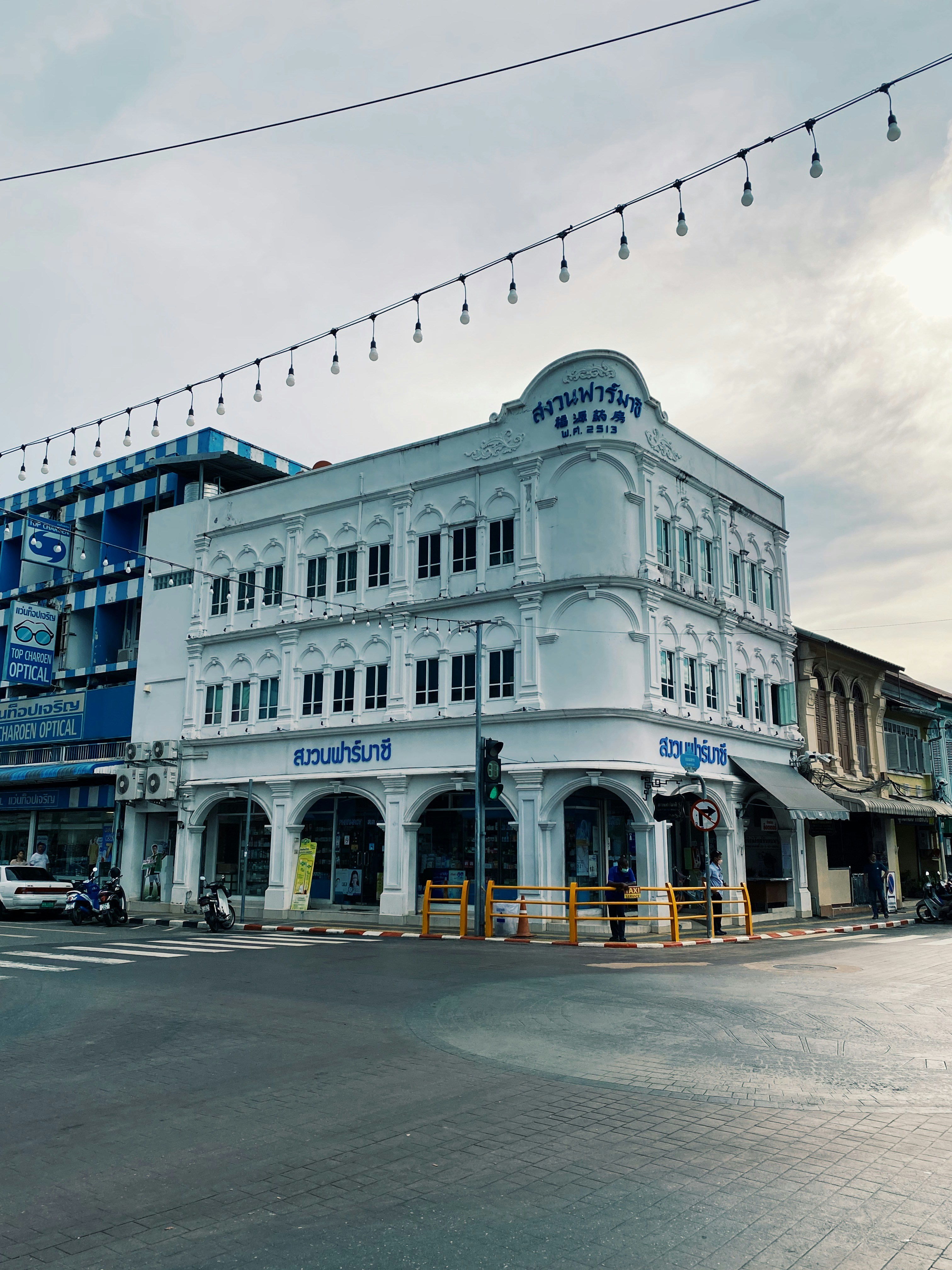 Historic white building with arched windows stands at a street corner under a string of lights.