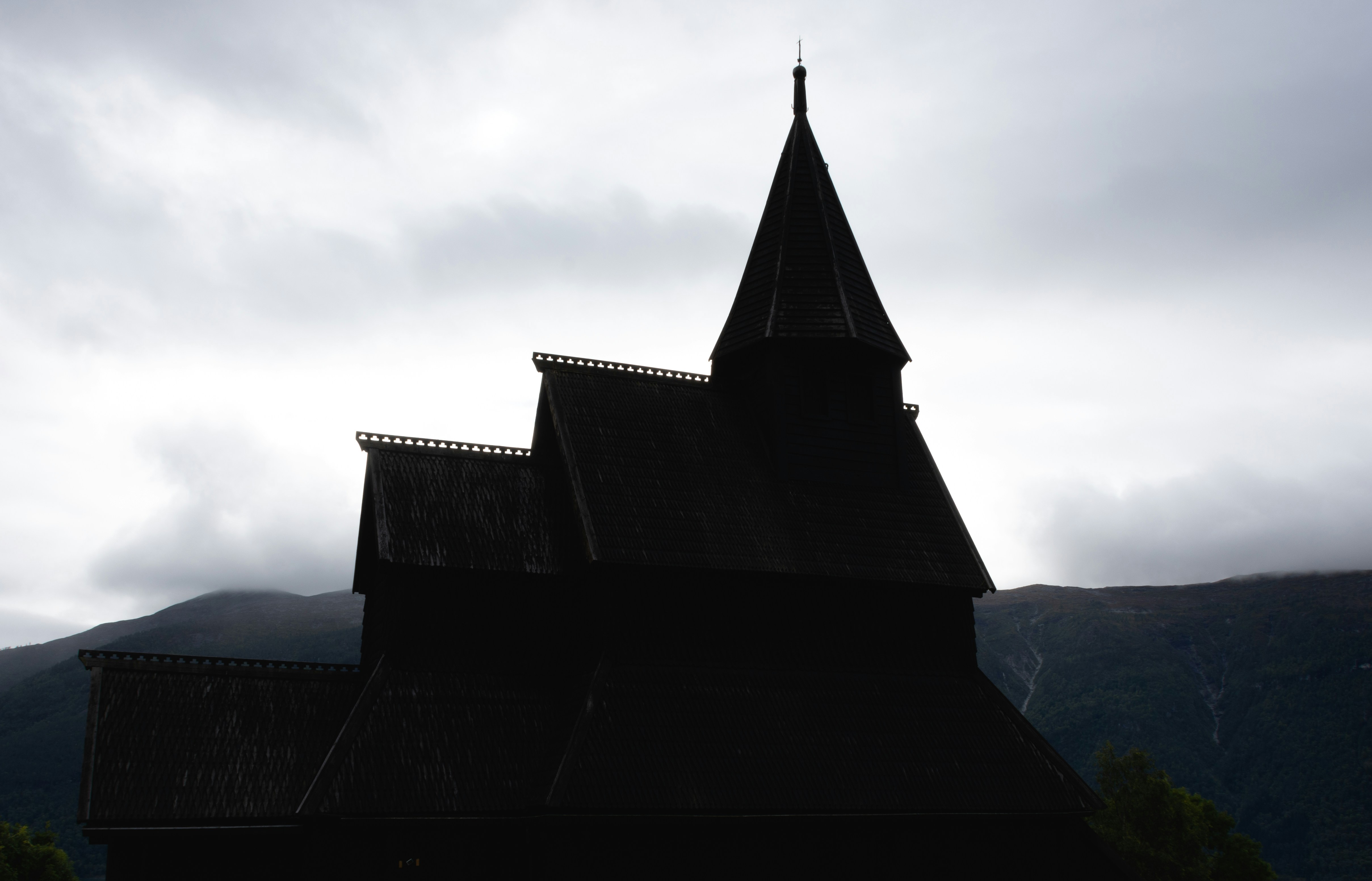A dark wooden structure with a pointed roof stands against a moody sky, evoking a sense of mystery and history.