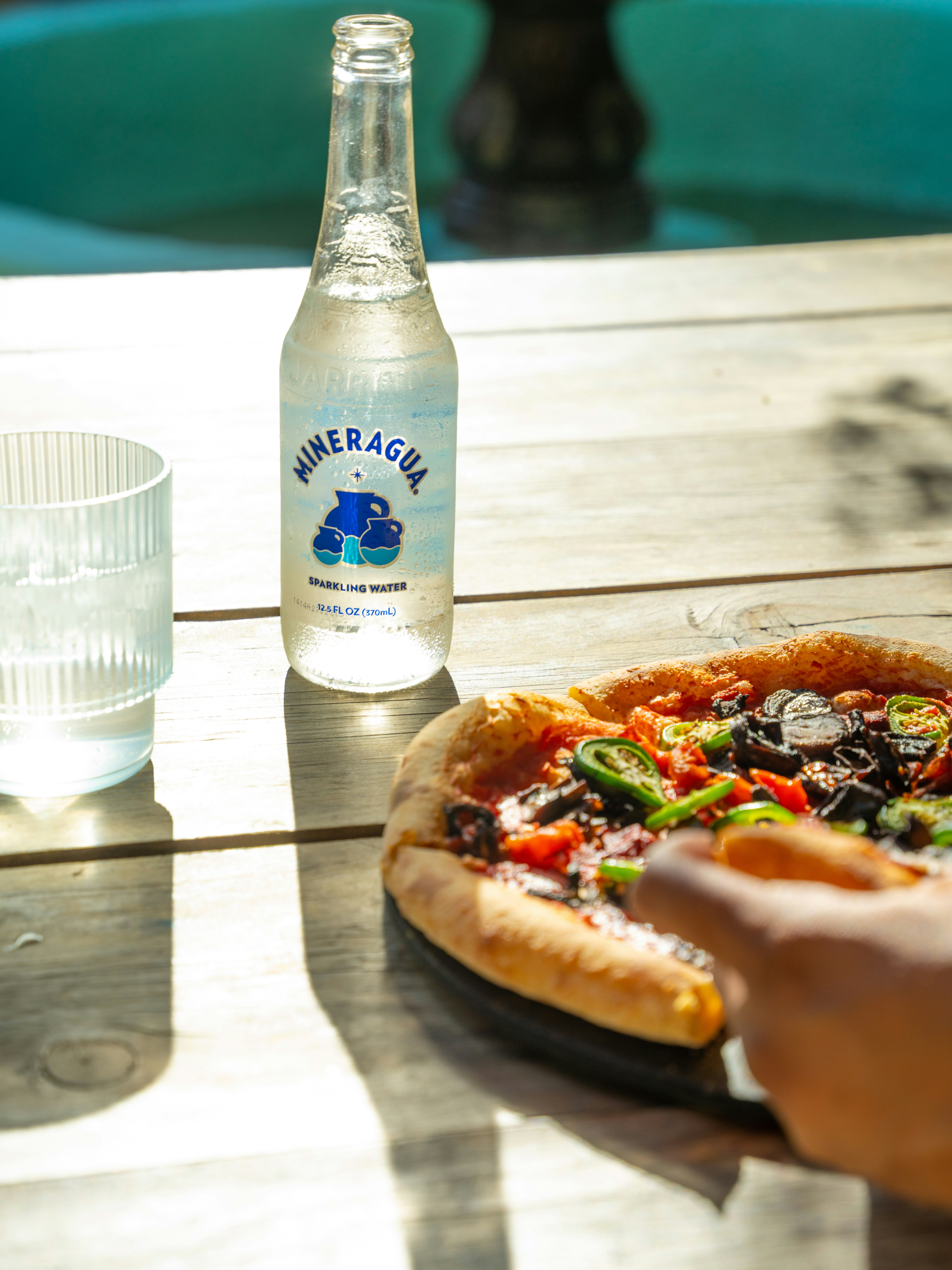 A pizza sitting on top of a wooden table next to a bottle of water ...